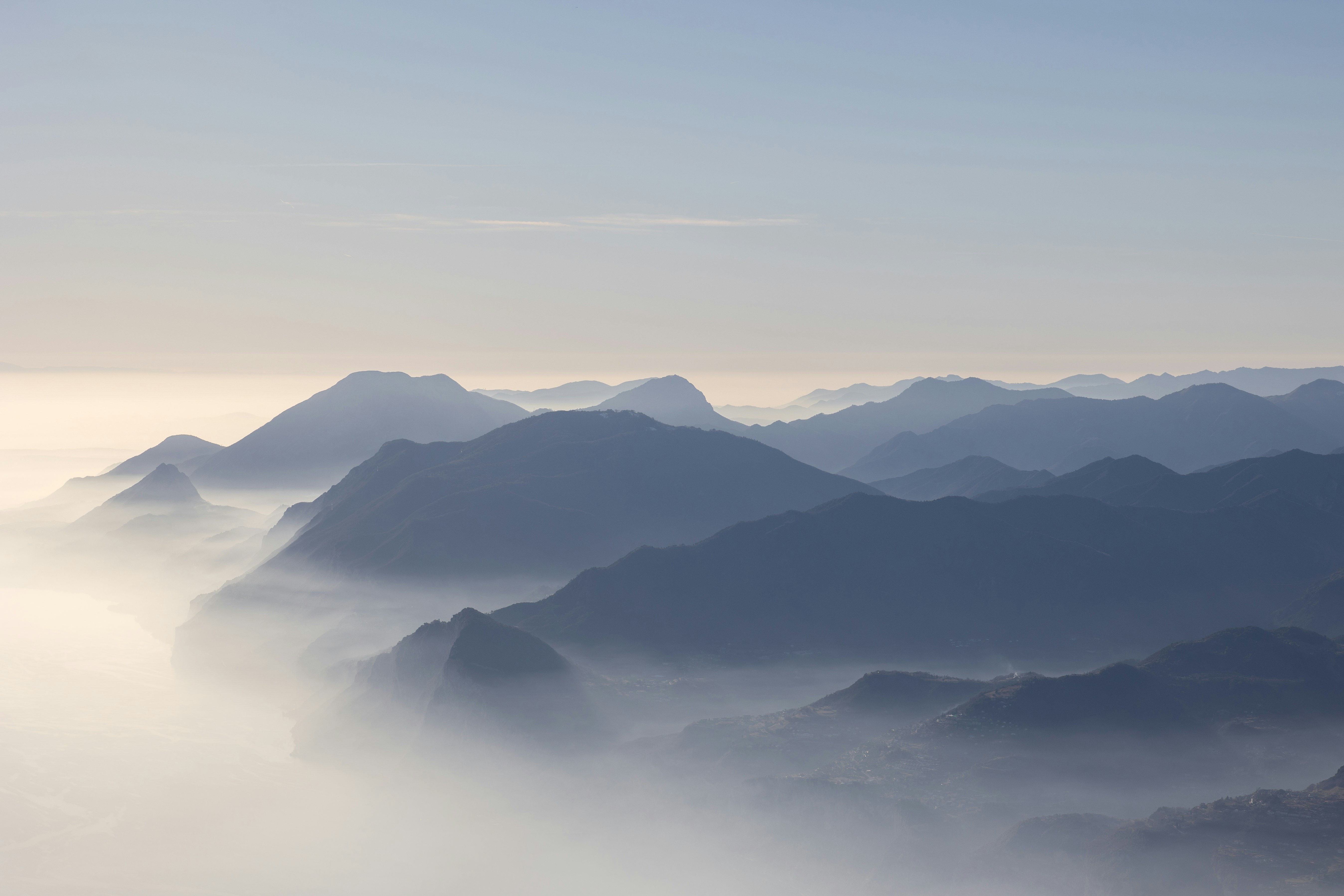Mountain range enveloped in soft mist under a clear morning sky.