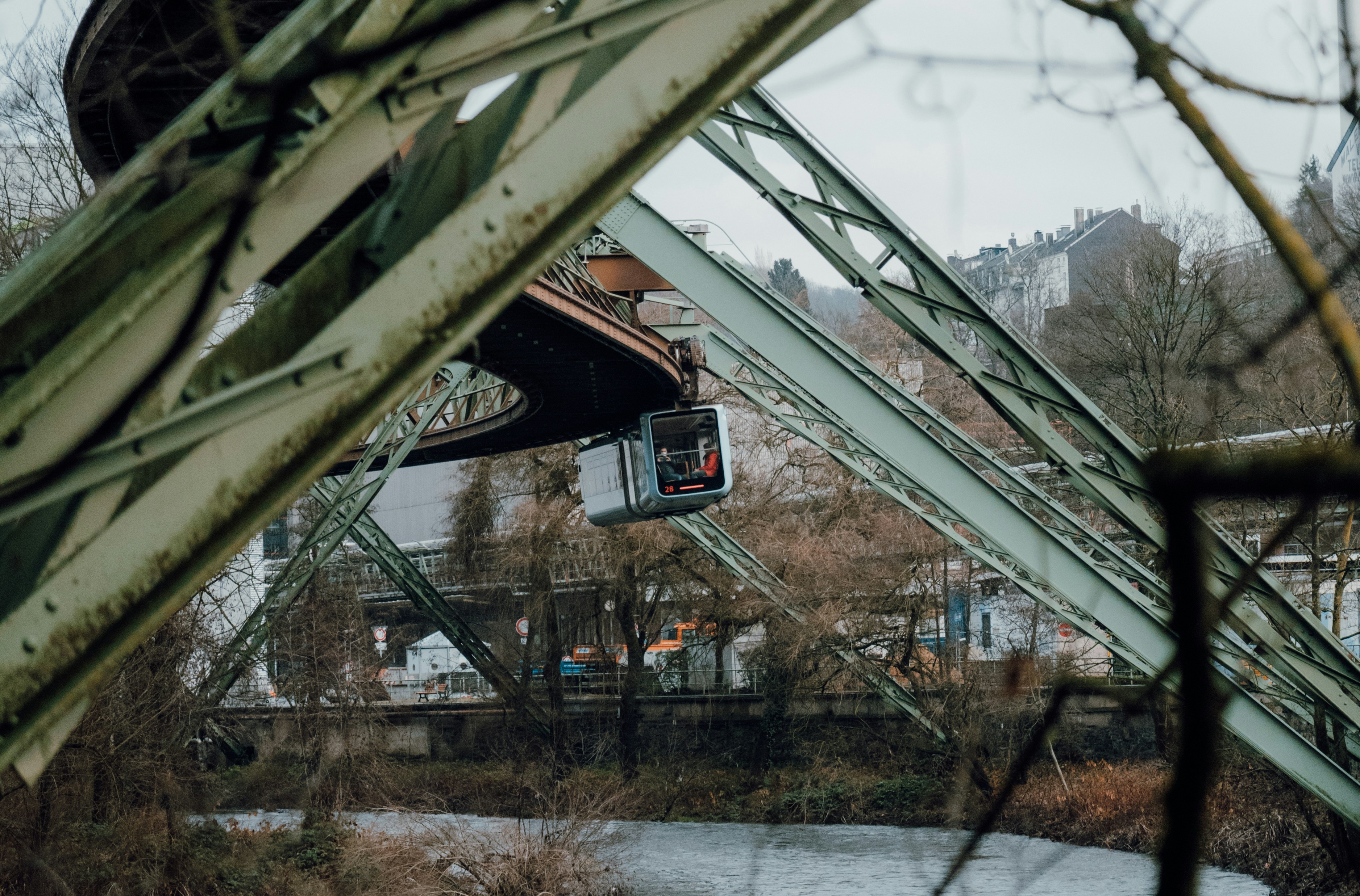 Suspended train gliding above a river amidst steel bridge structures.