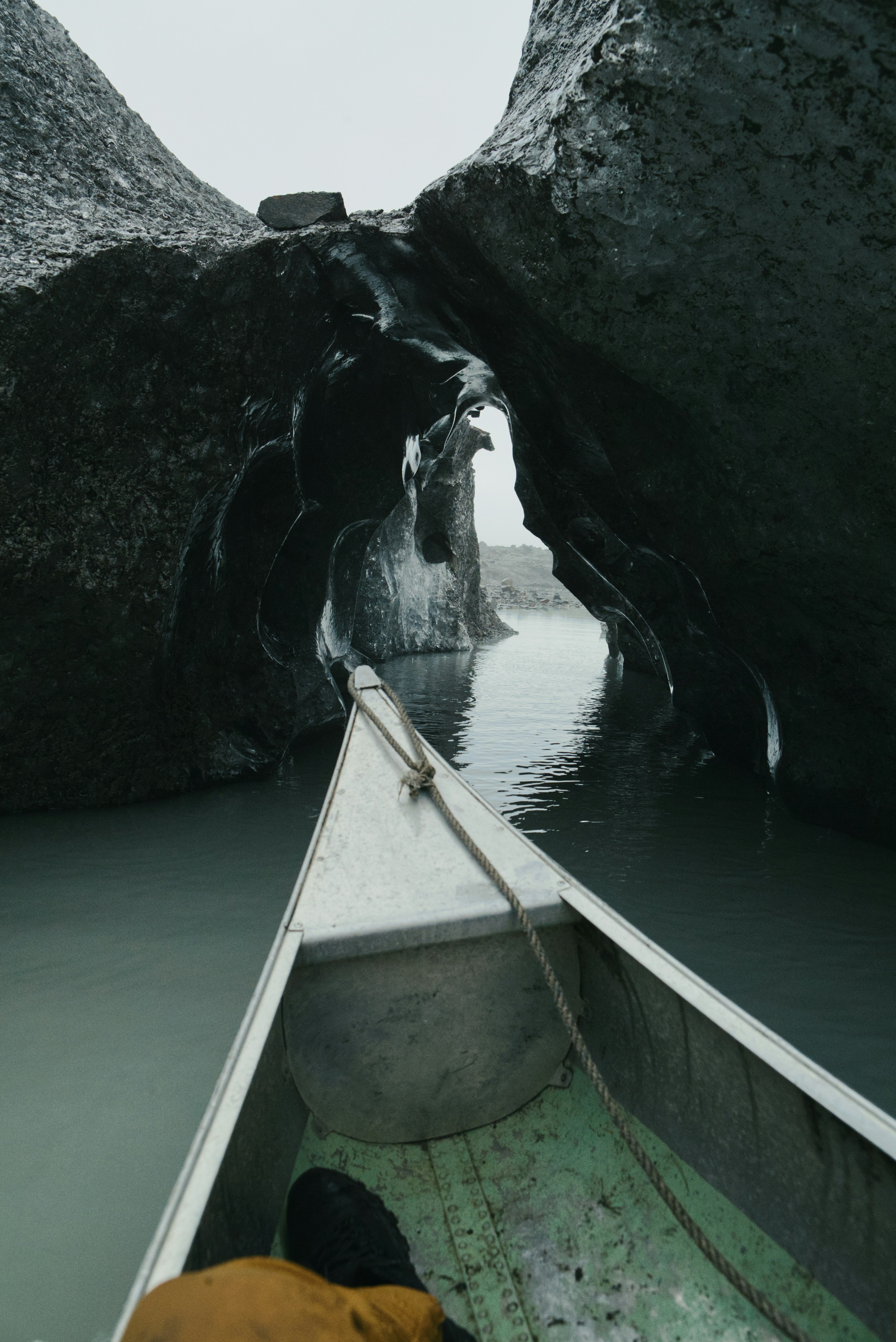 A canoe glides through a rocky archway, revealing a misty landscape beyond. The serene waters reflect the rugged textures of the surrounding cliffs.