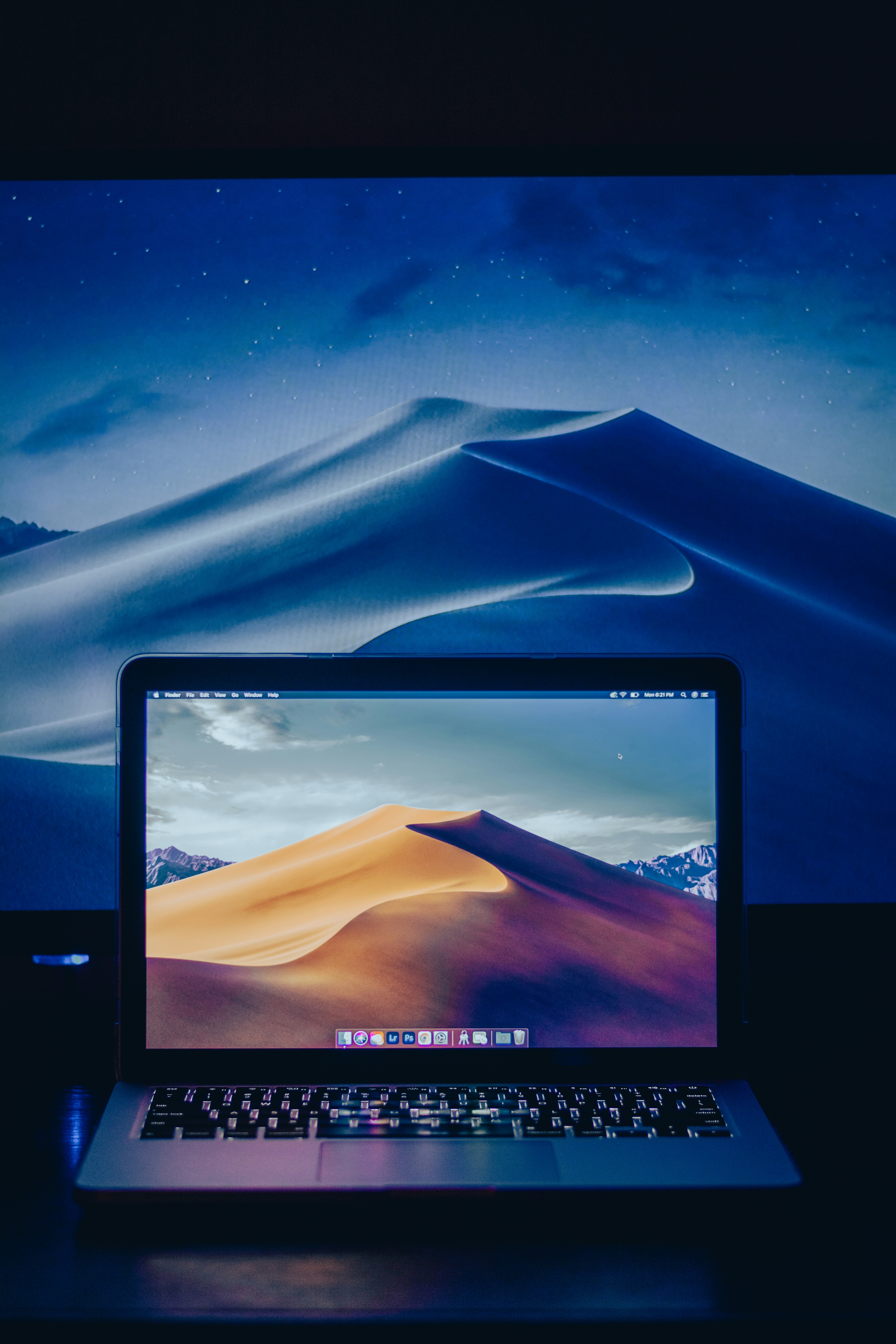A laptop displaying a desert landscape sits in front of a larger screen showcasing the same scene, creating a seamless digital experience.
