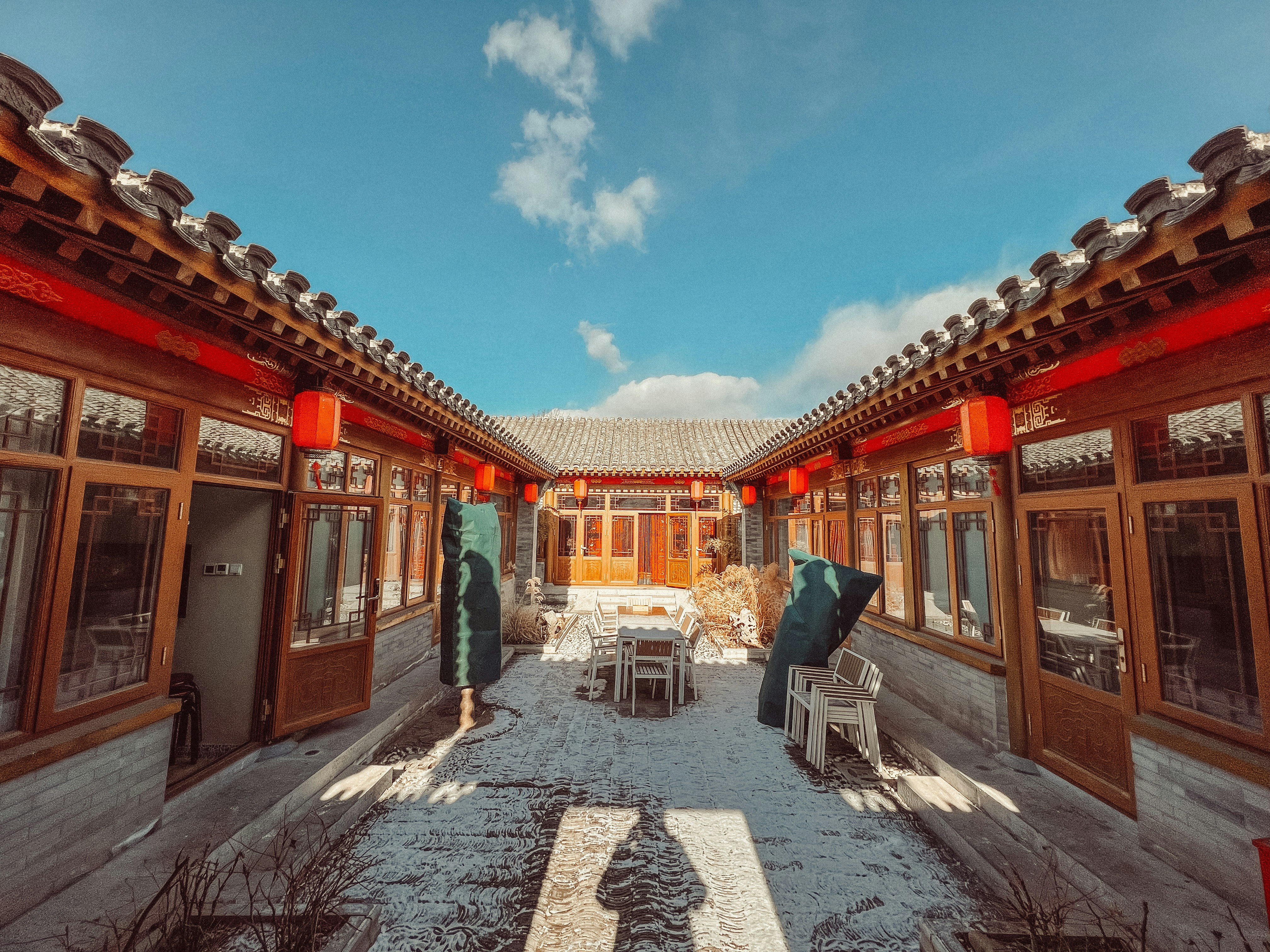 Traditional Chinese courtyard featuring wooden architecture and snow-covered ground, with vibrant lanterns adorning the eaves. A tranquil setting invites relaxation.