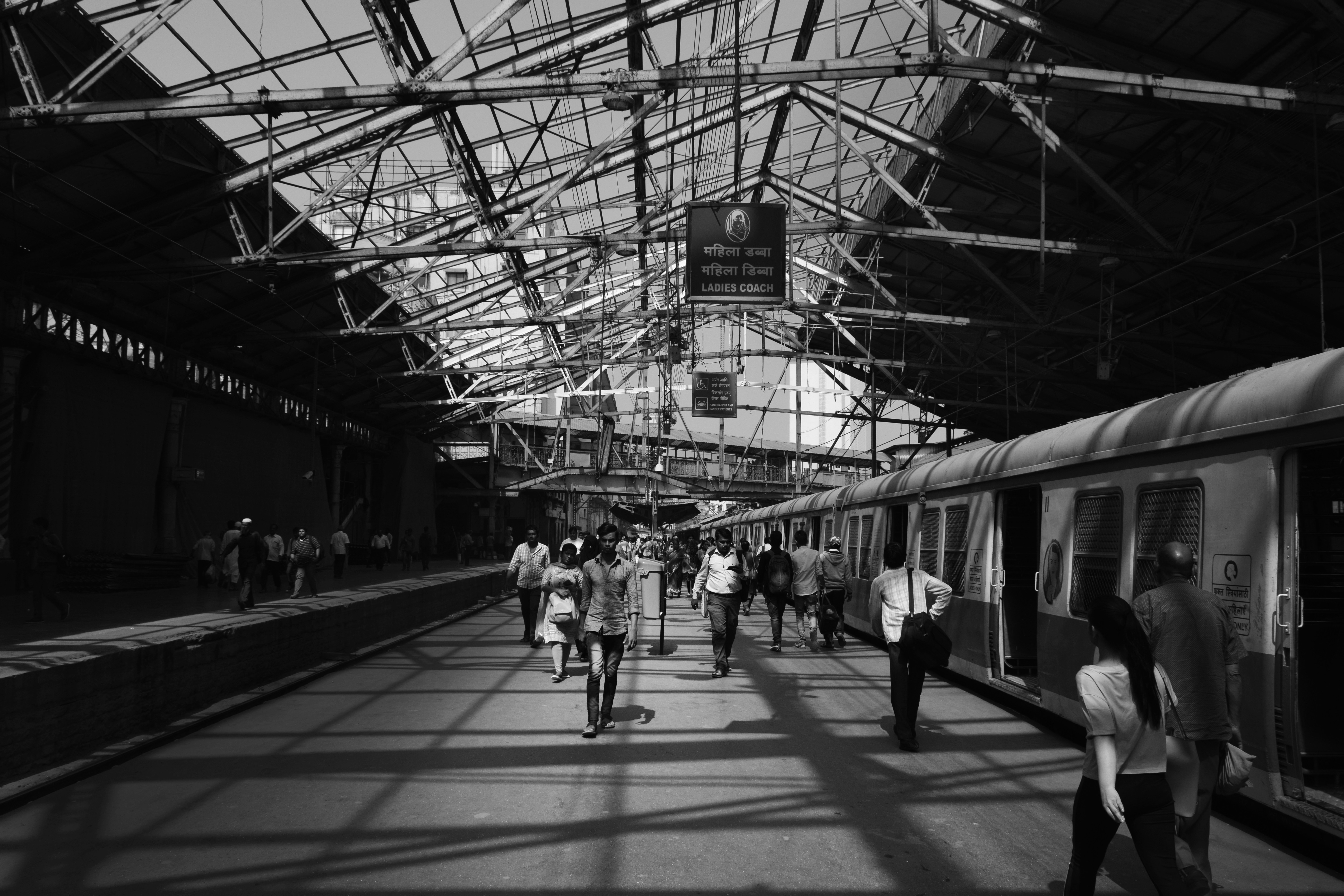 Commuters walking through a sunlit train station with industrial architecture.