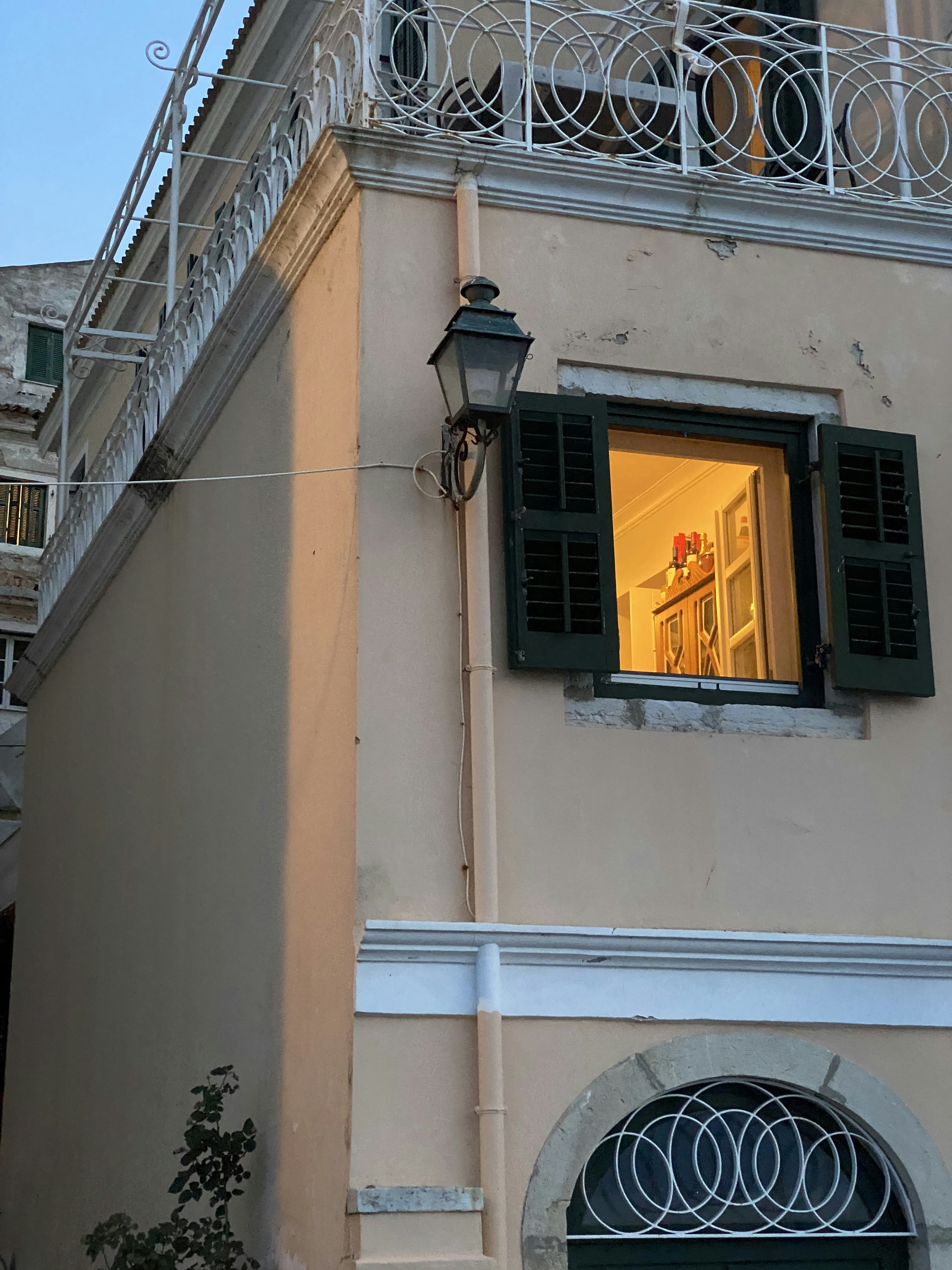 Golden Glow Through Green Shutters: A Corner Facade with Wrought-Iron Balcony