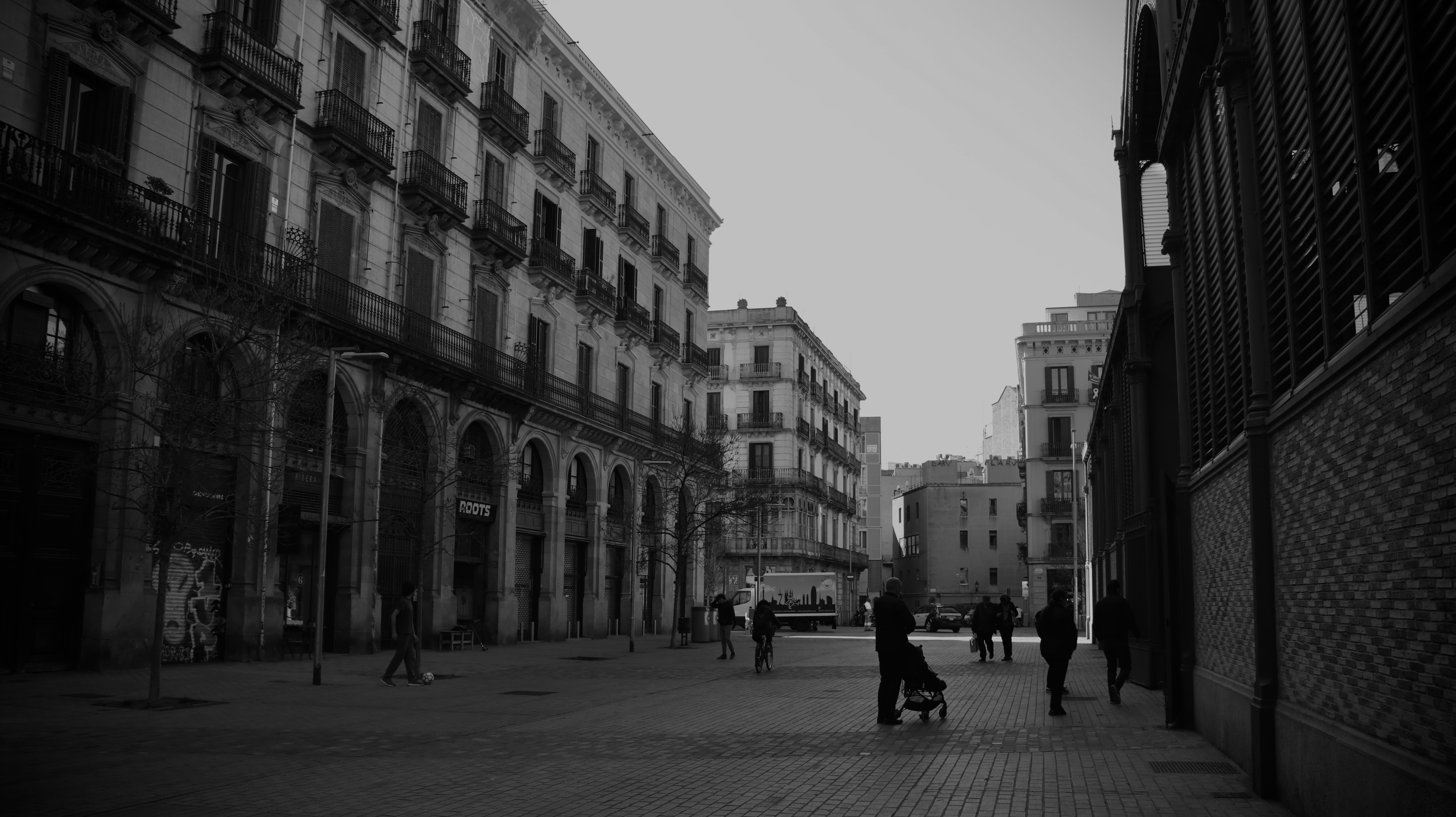 Black and white scene of a historic street with people walking, showcasing architectural details and urban life.