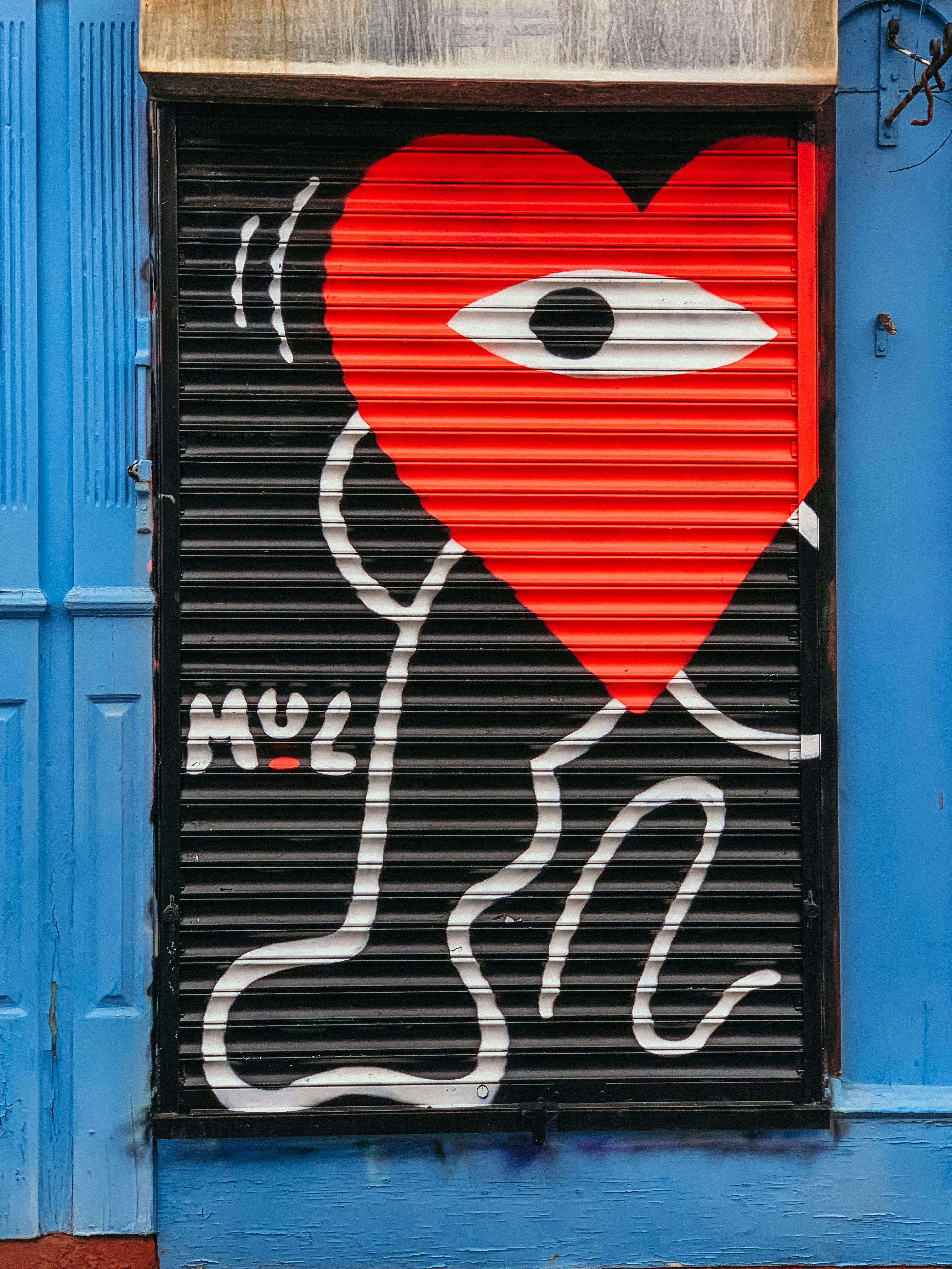 Vibrant mural featuring a large red heart with an eye, set against a blue background, embodying playful street art. The design incorporates fluid lines and a whimsical character.