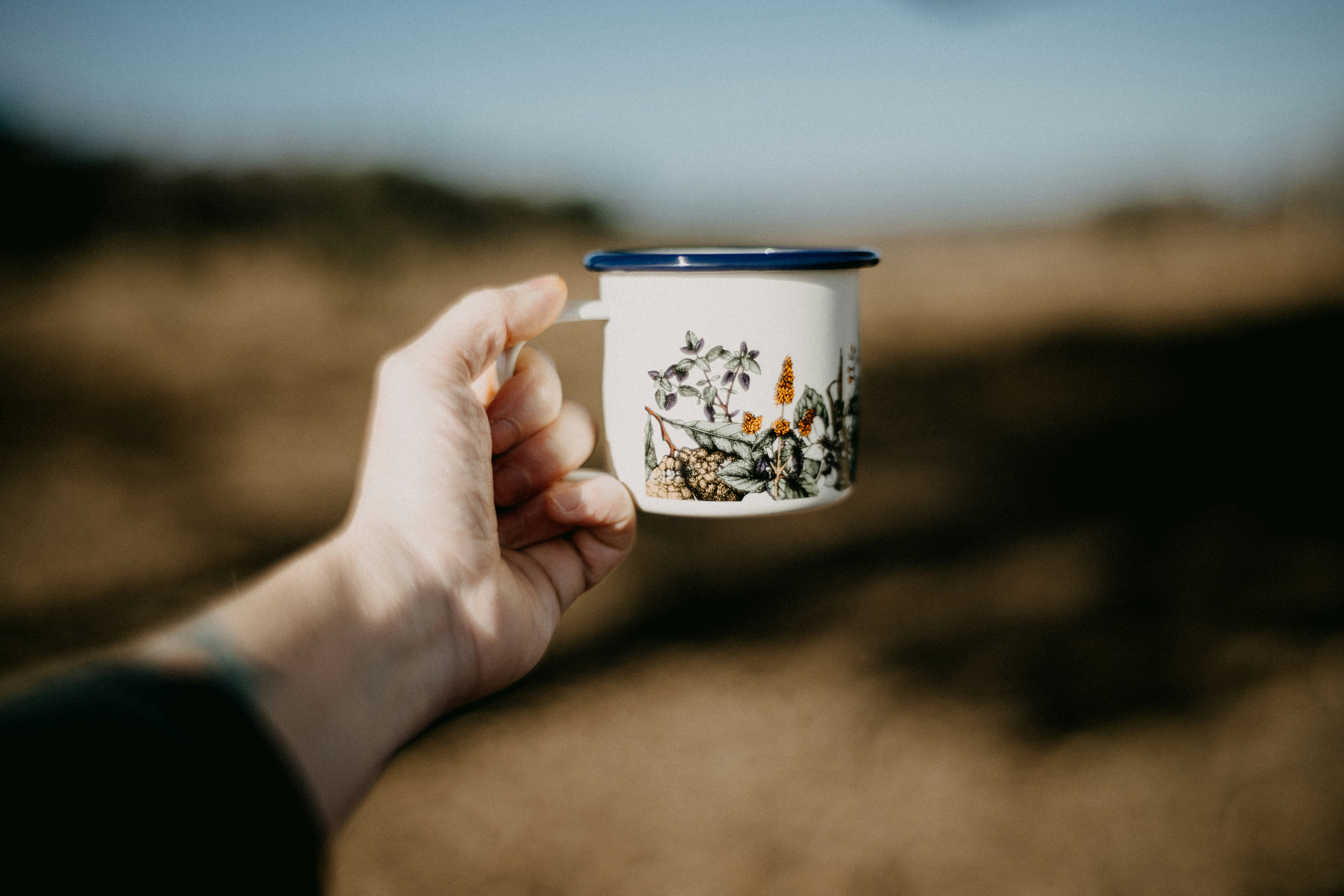 Floral Ceramic Mug in a Sunlit Field: A Hand-Held Moment