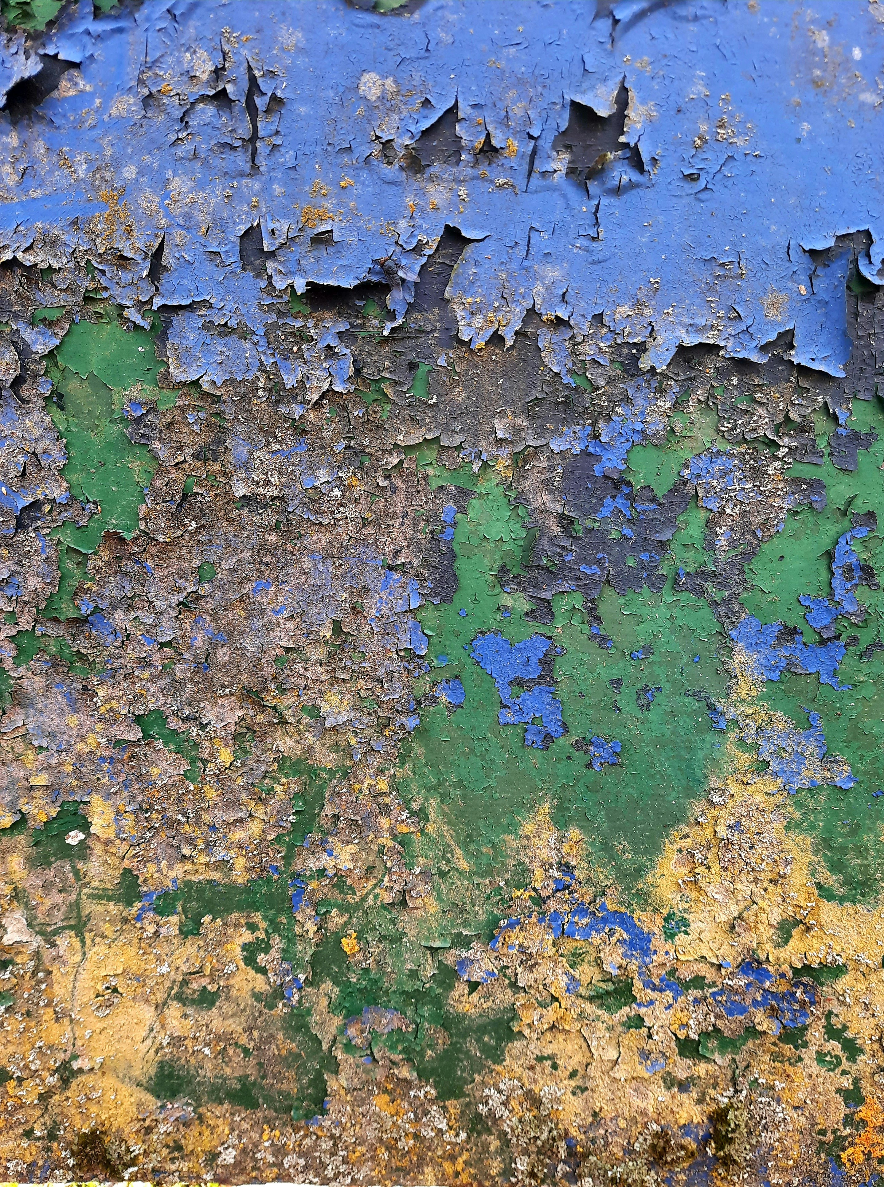 Close-up of a weathered surface showcasing vibrant blue and green paint peeling away to reveal textures and colors beneath.