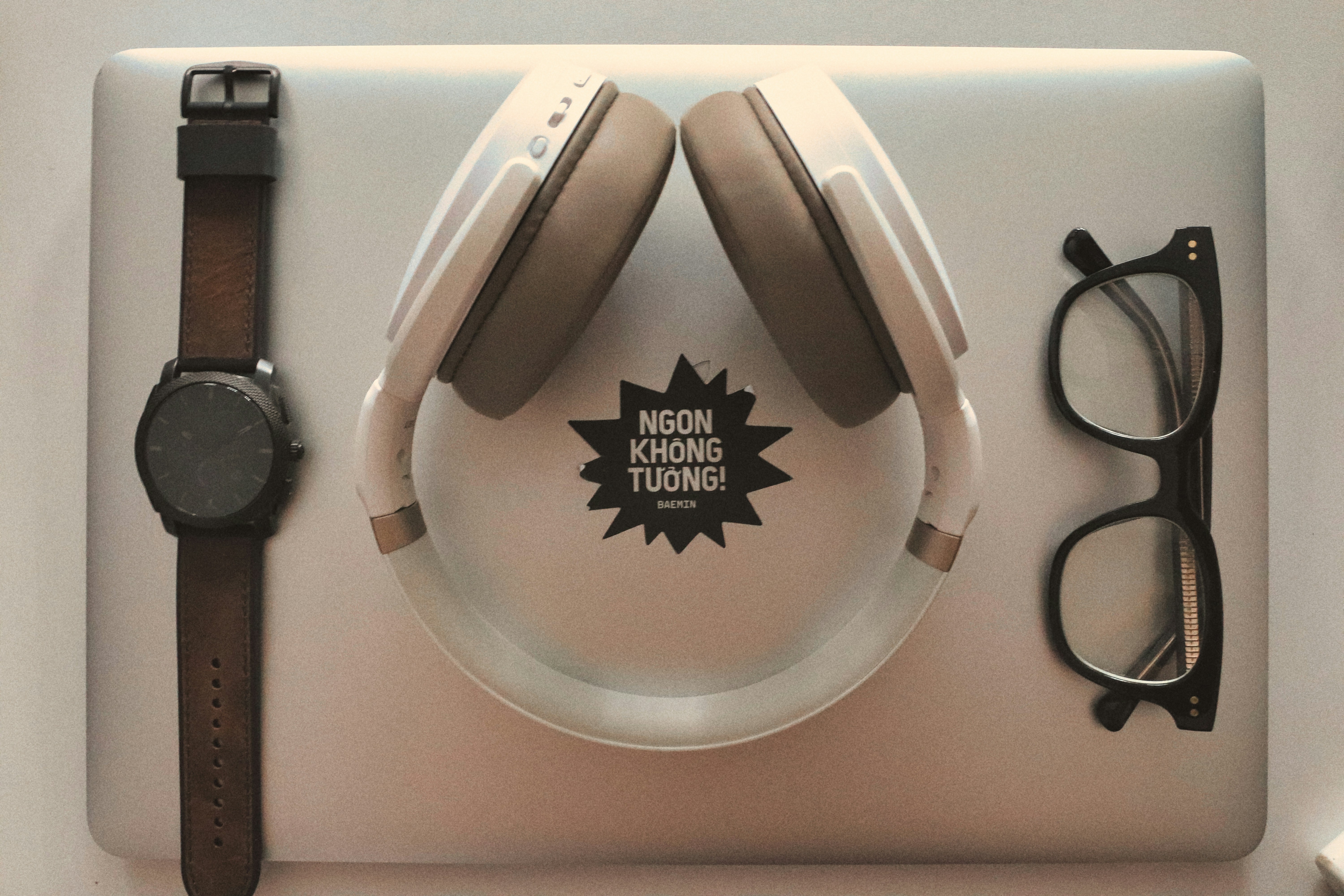 Centered Halo: White Headphones Framed by Watch and Glasses on a Silver Laptop