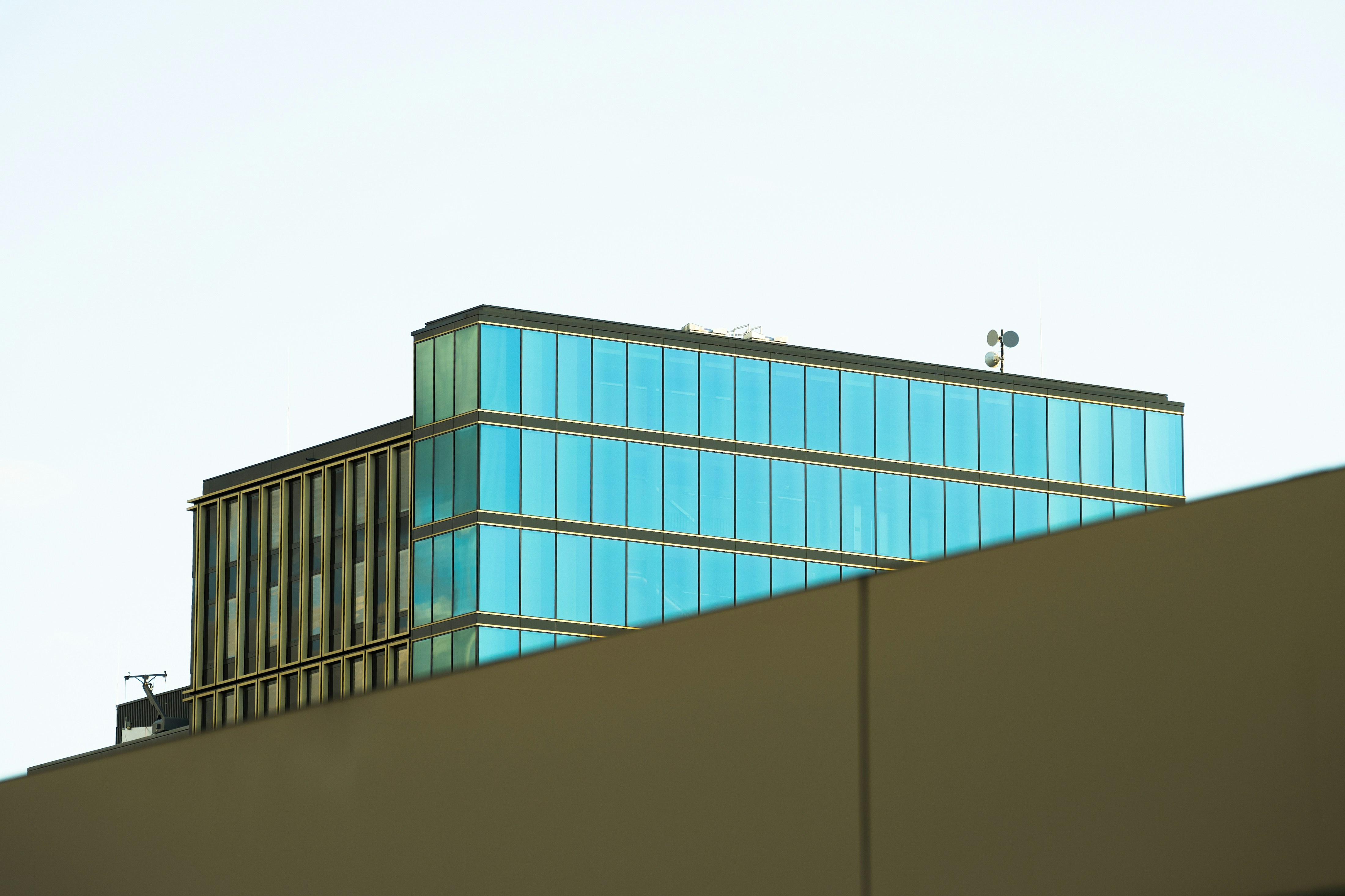 Modern building with reflective blue windows against a minimalist foreground wall under a clear sky.