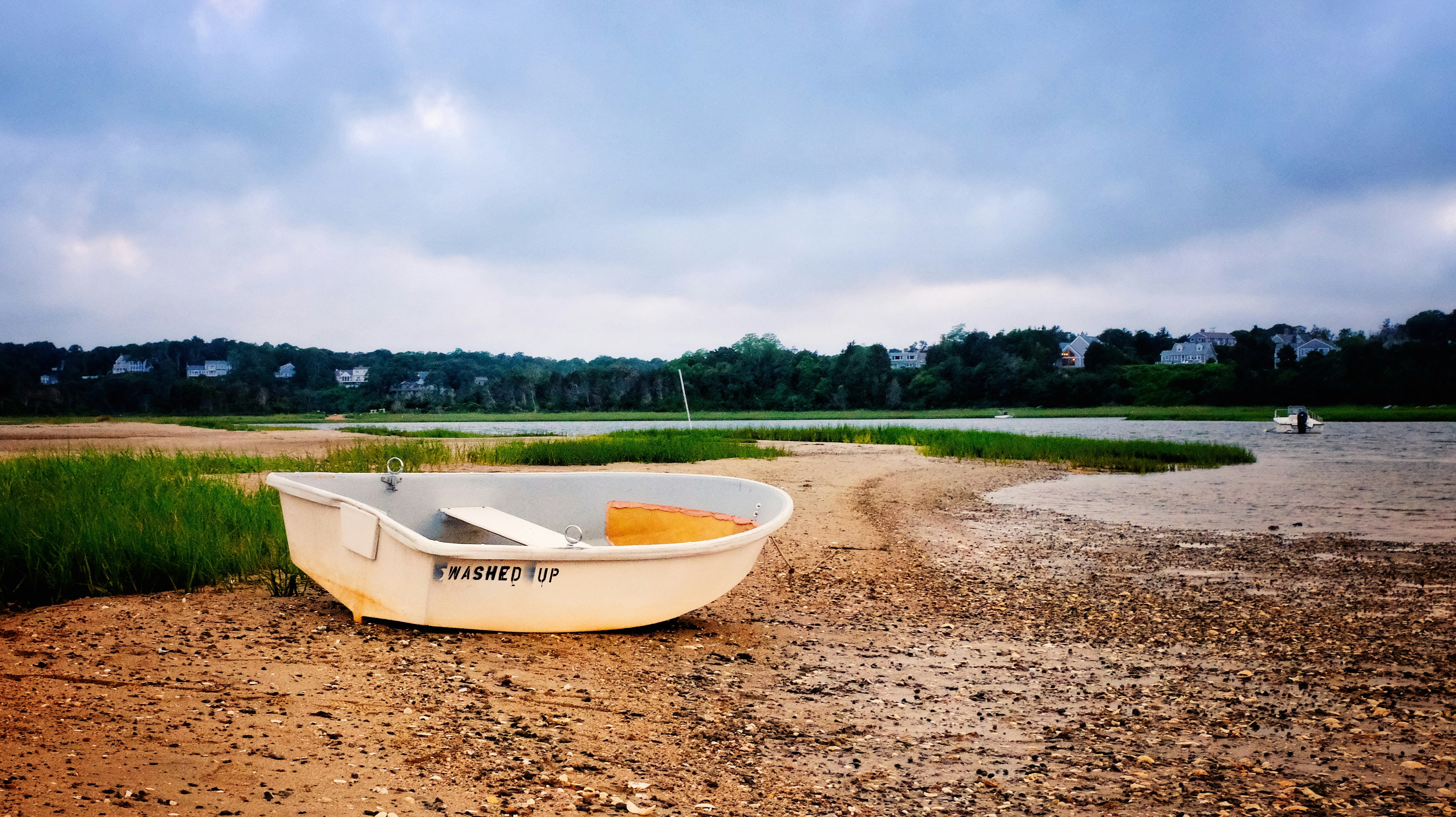 A little dingy called "Washed Up" on a bay near Orleans, Massachusetts, on Cape Cod | a white boat sitting on top of a sandy beach