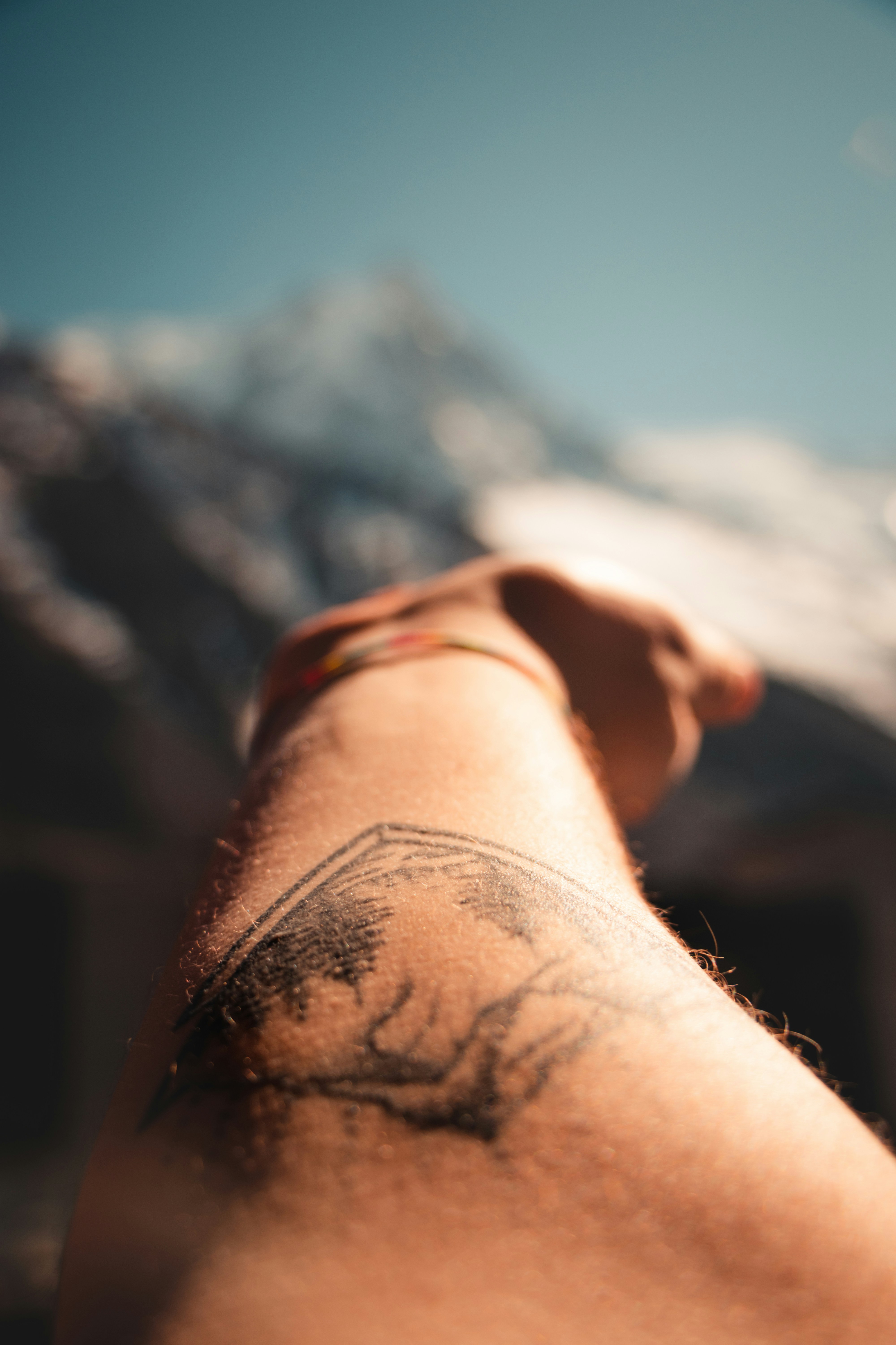 Alpine Reach: Tattooed Forearm Extending Toward Snow-Capped Peaks