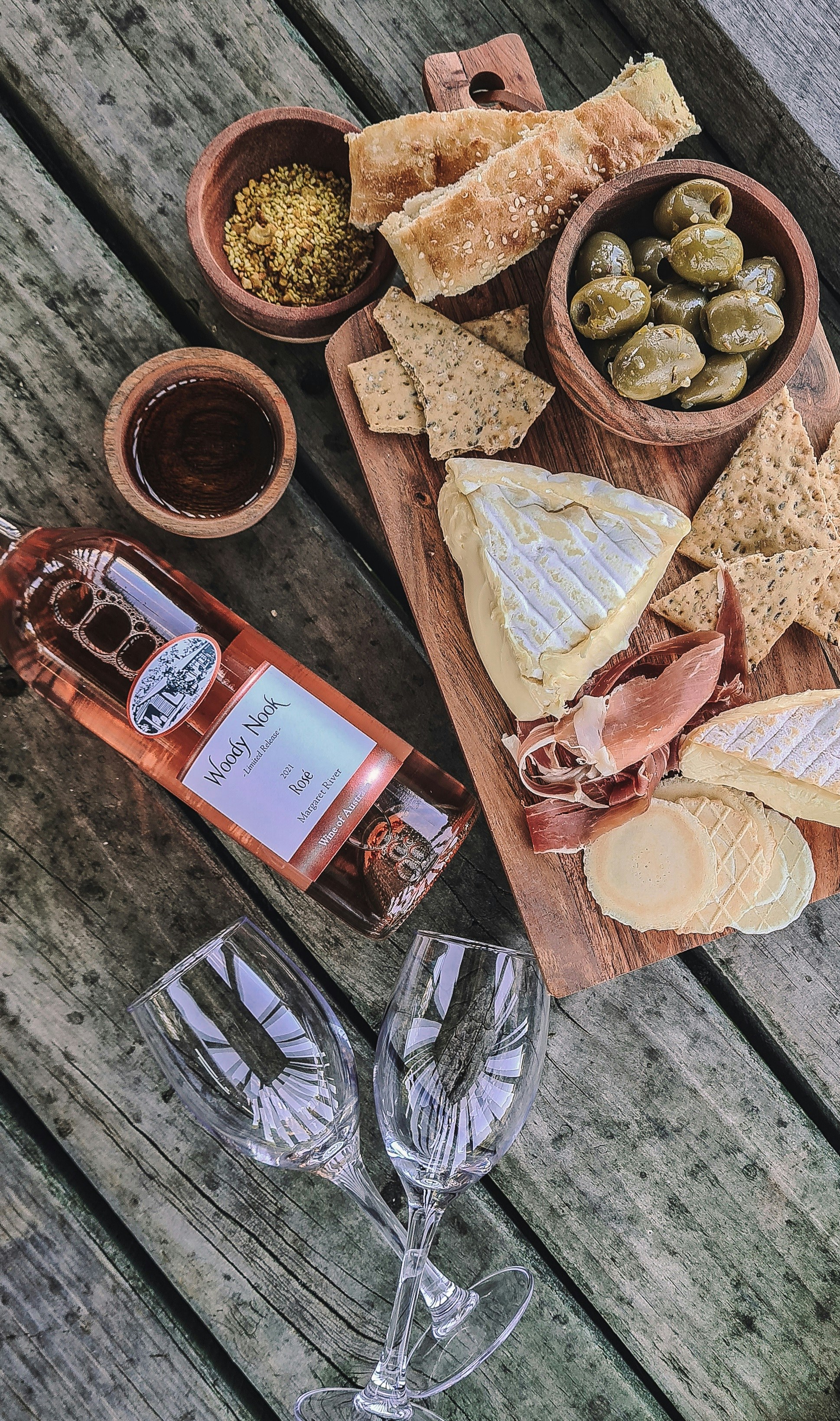 A beautifully arranged charcuterie board featuring various cheeses, olives, crackers, and a bottle of rosé wine, complemented by elegant wine glasses.