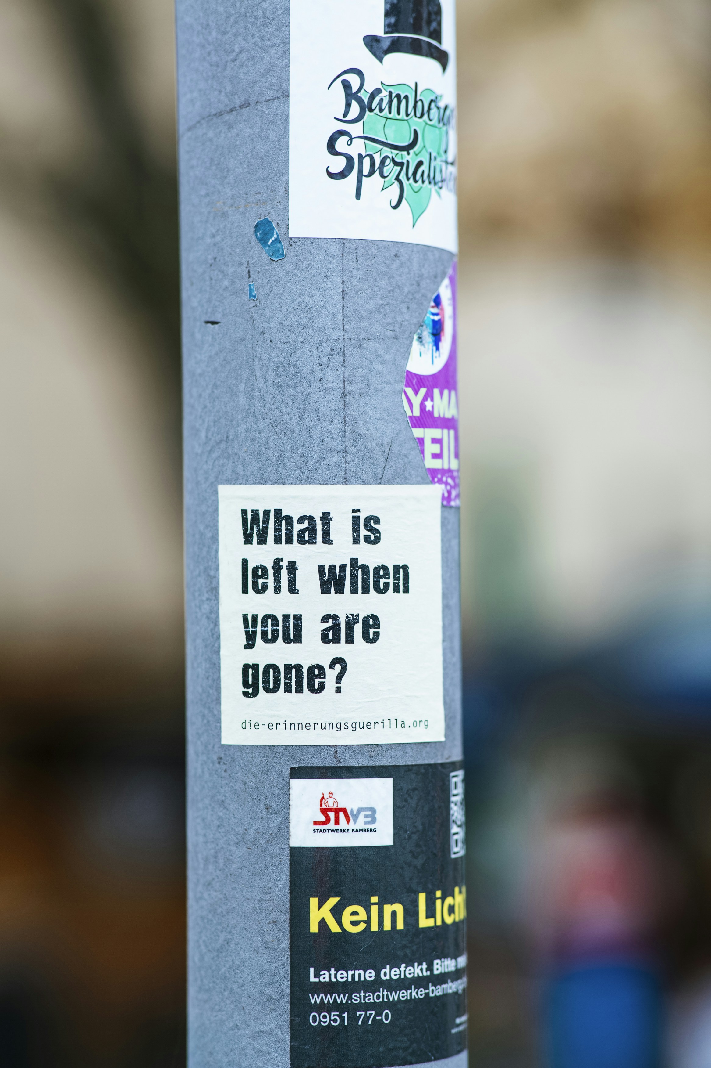 A thought-provoking sticker on a pole asking, 'What is left when you are gone?' alongside other local advertisements and messages.