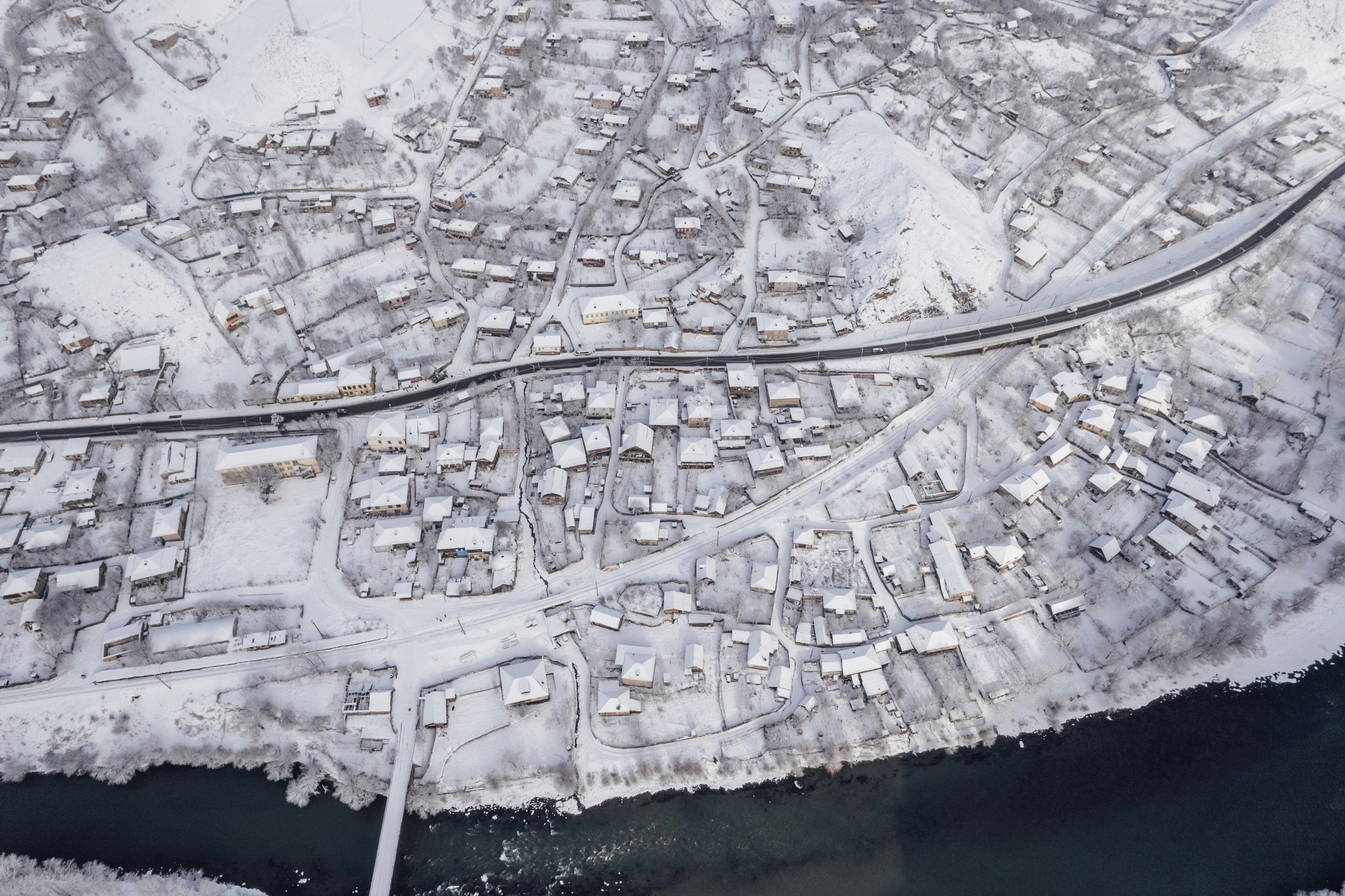 Aerial view of a quaint village blanketed in snow, showcasing the intricate layout of houses and roads amidst a serene winter landscape.