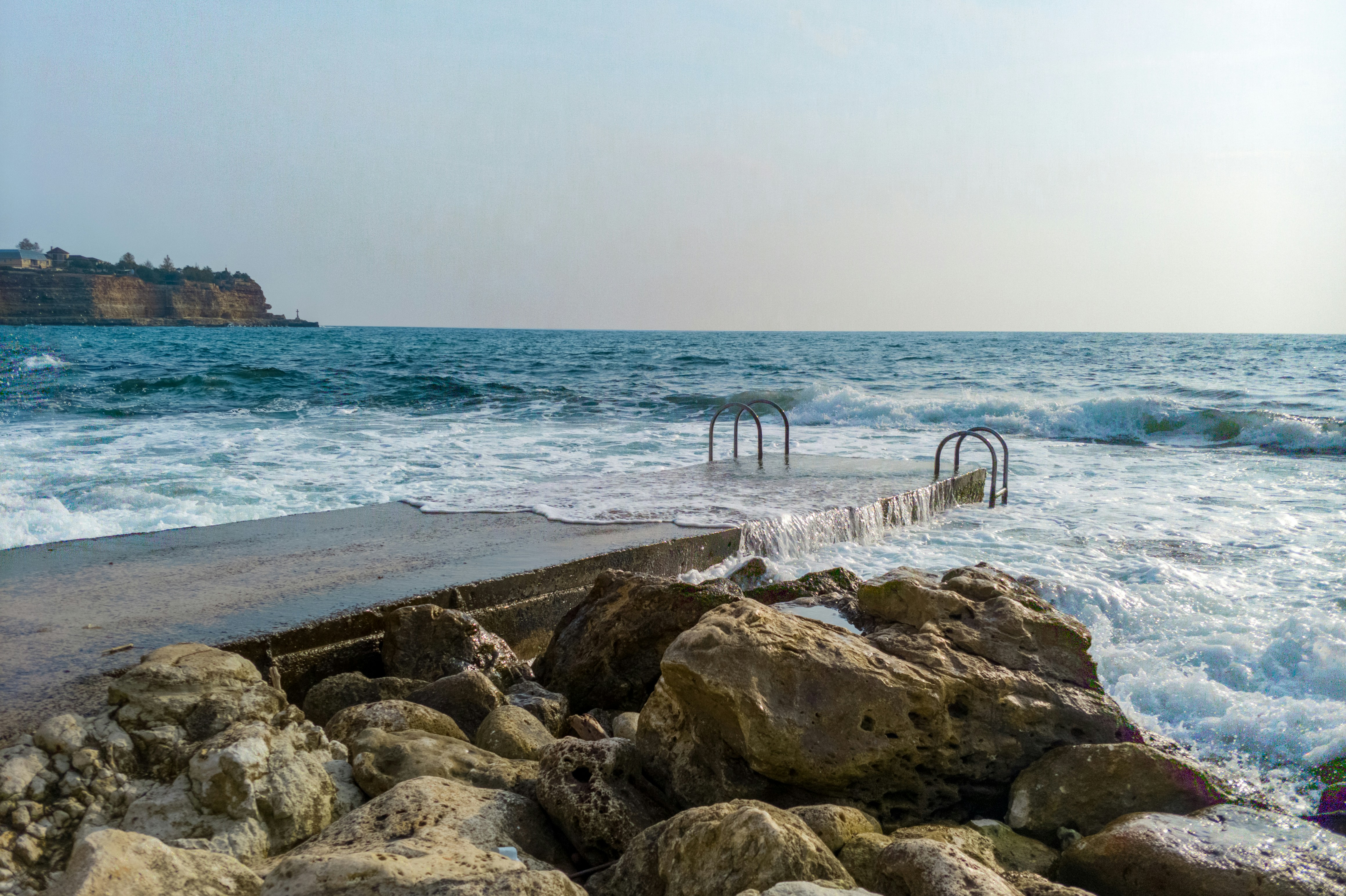 Concrete pier extending into turbulent waters, framed by rocky shoreline under a hazy sky.