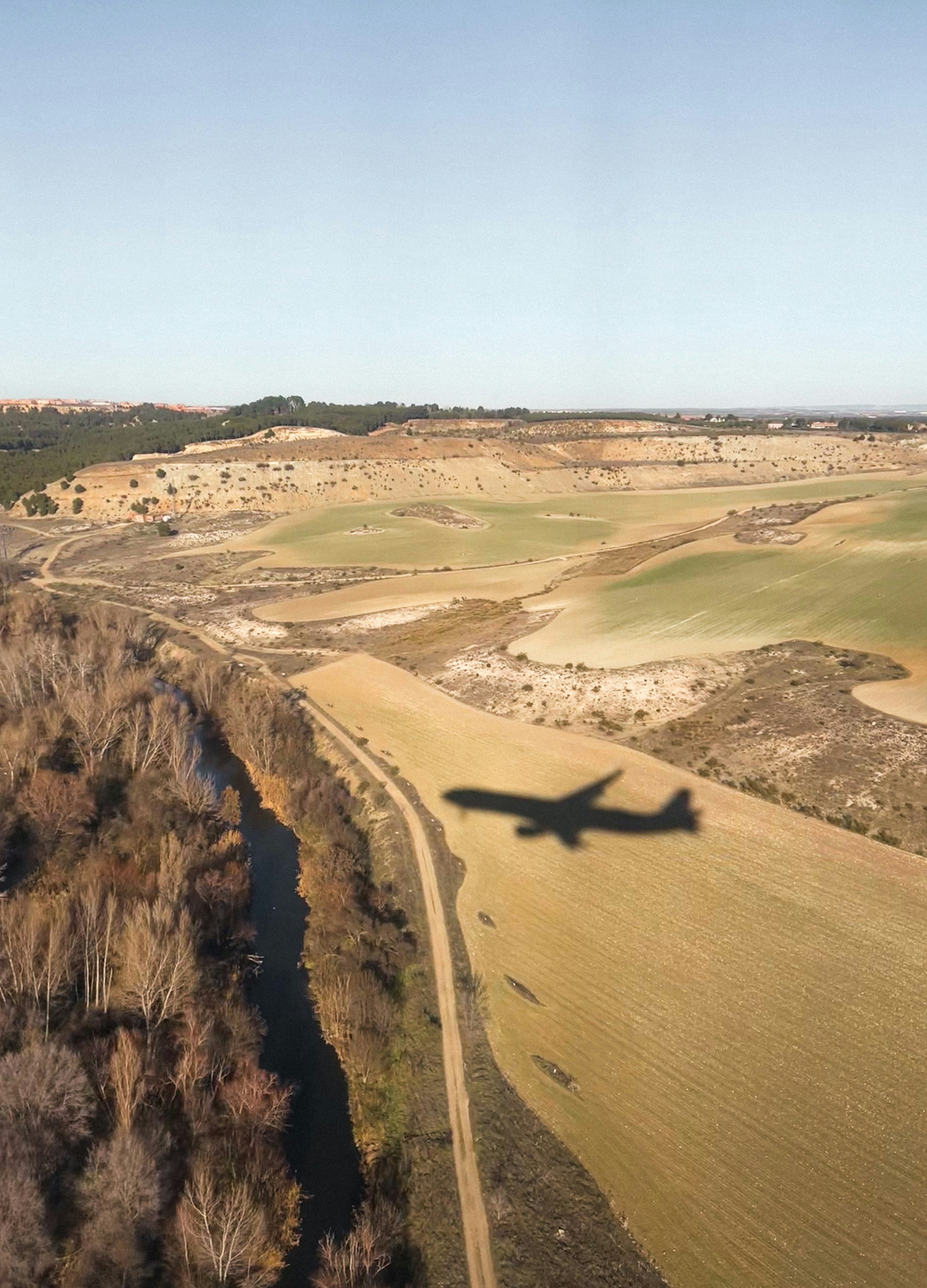 The shadow of an airplane glides over a patchwork of fields and a winding river, capturing the interplay between flight and earth. 
