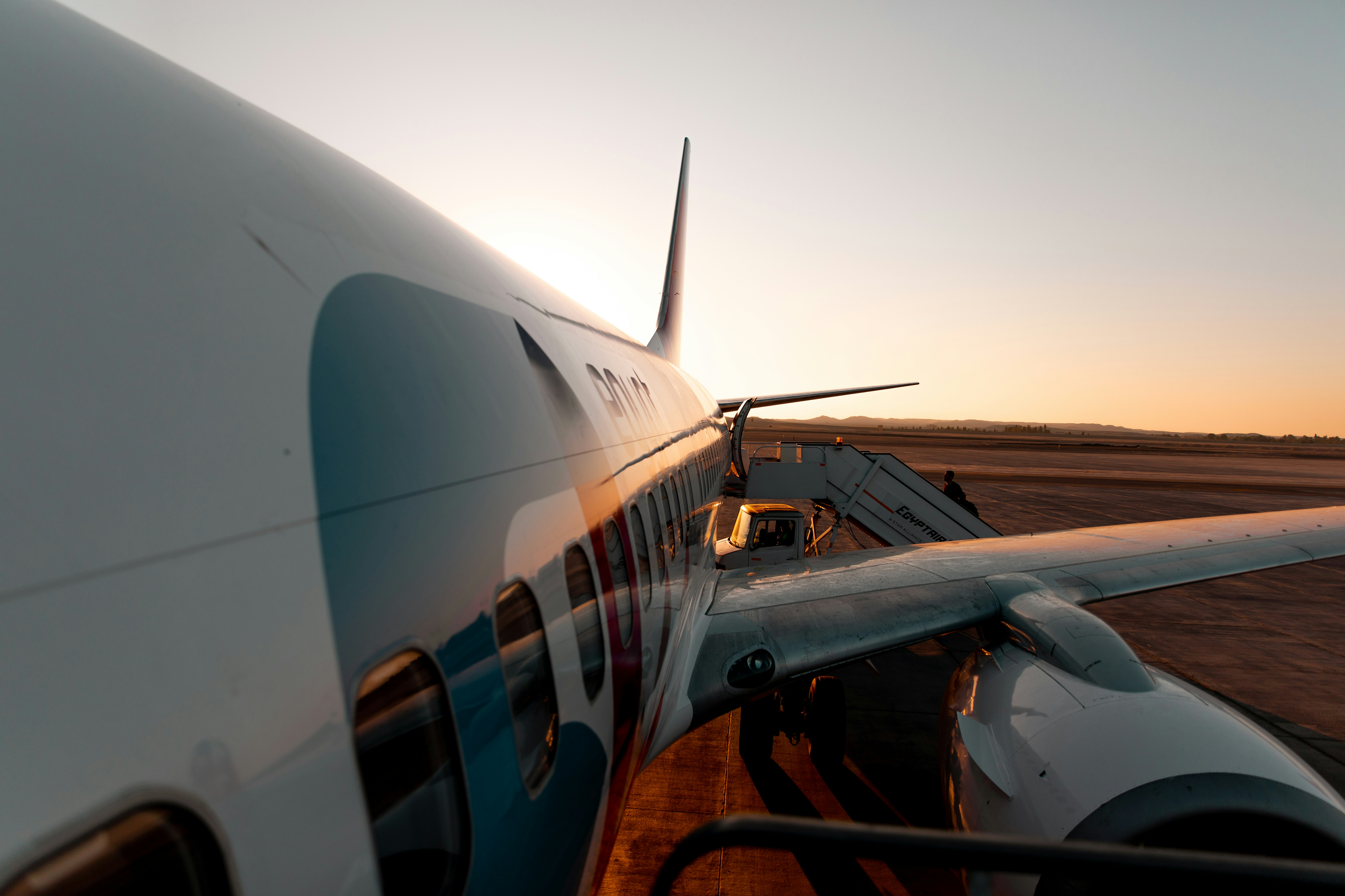 Airplane parked on the tarmac at sunrise, capturing the warm glow along its fuselage.