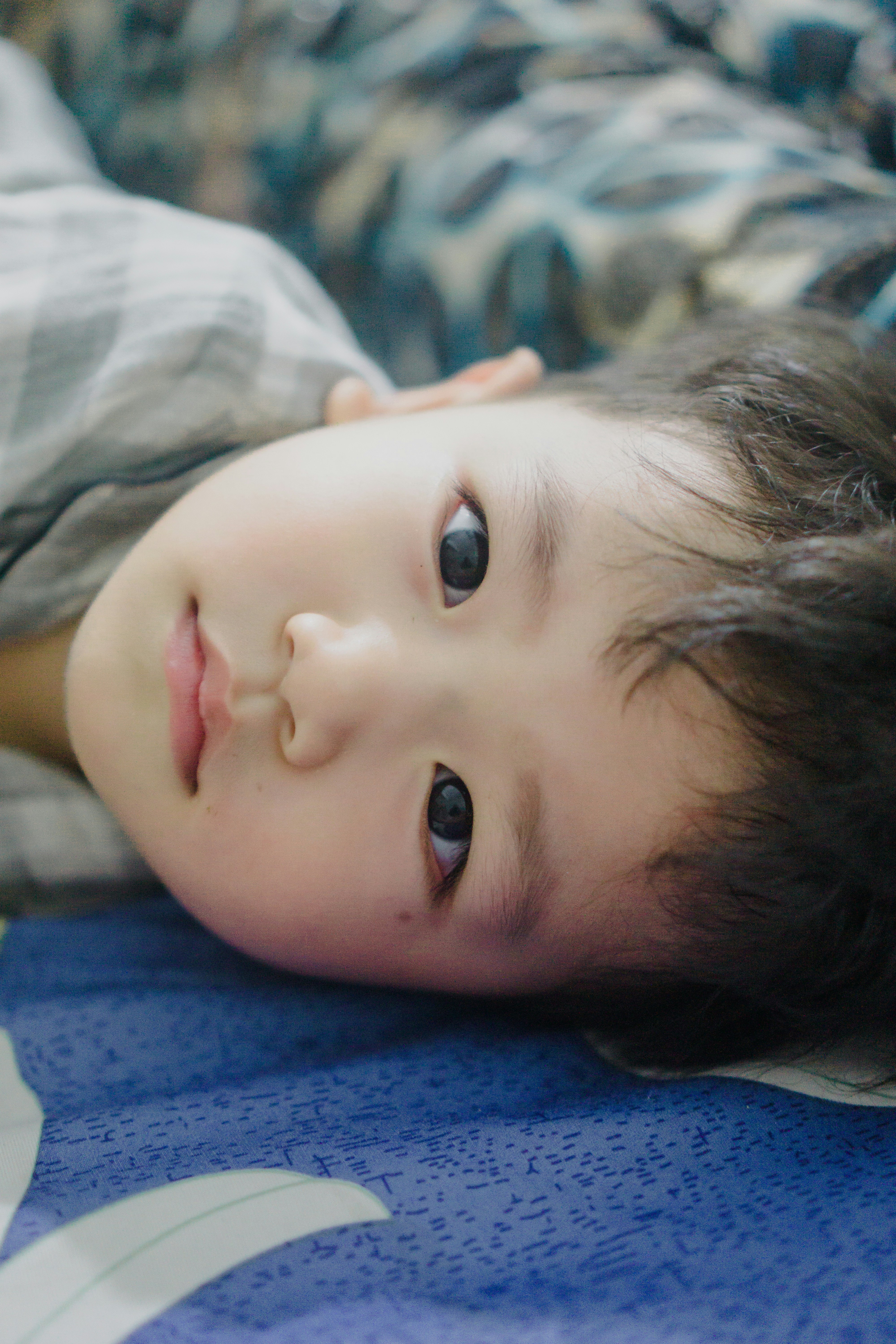 A young child gazes thoughtfully while lying on a patterned surface, capturing a moment of quiet reflection.
