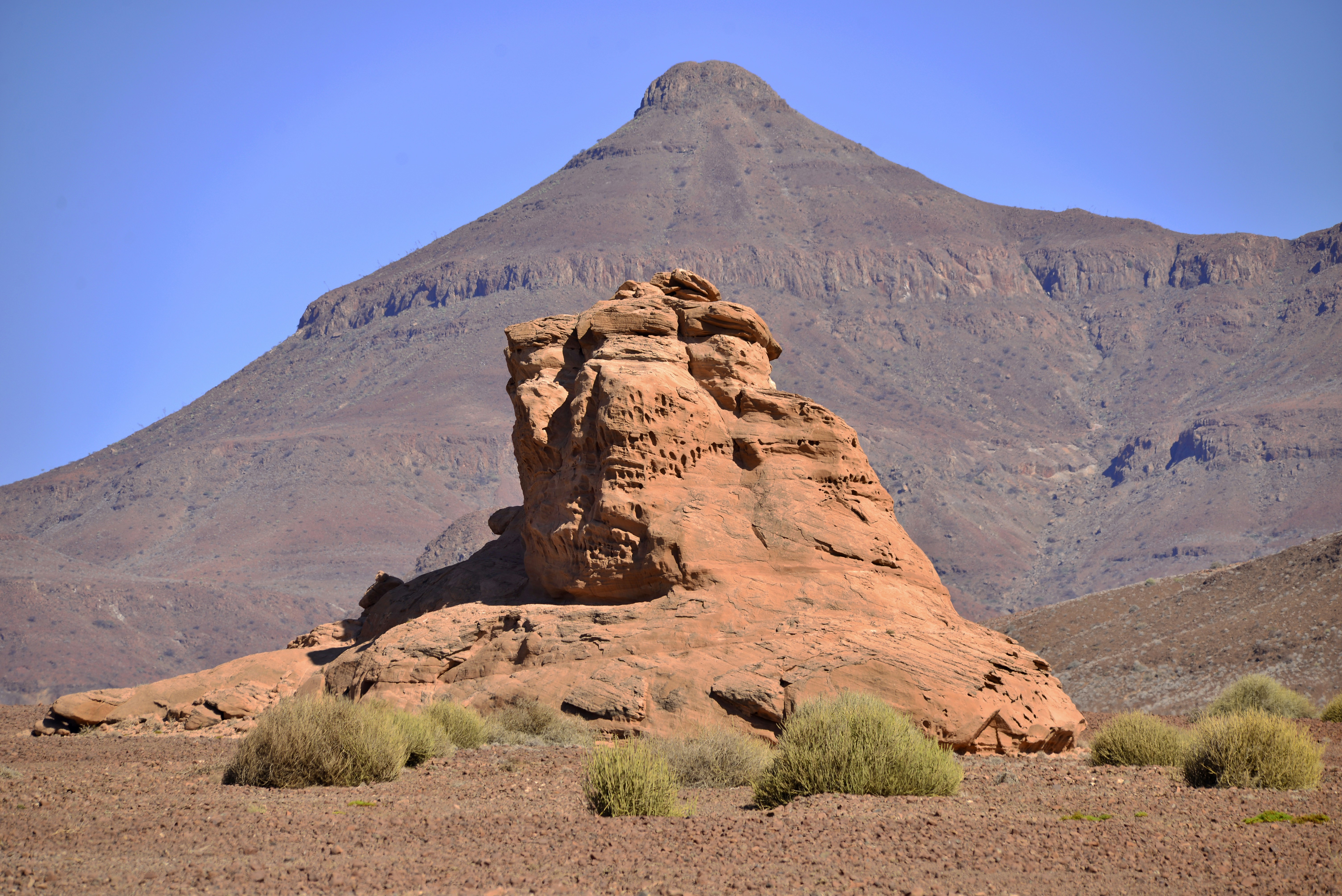 A striking rock formation stands defiantly against a backdrop of arid mountains, showcasing the rugged beauty of the desert landscape.