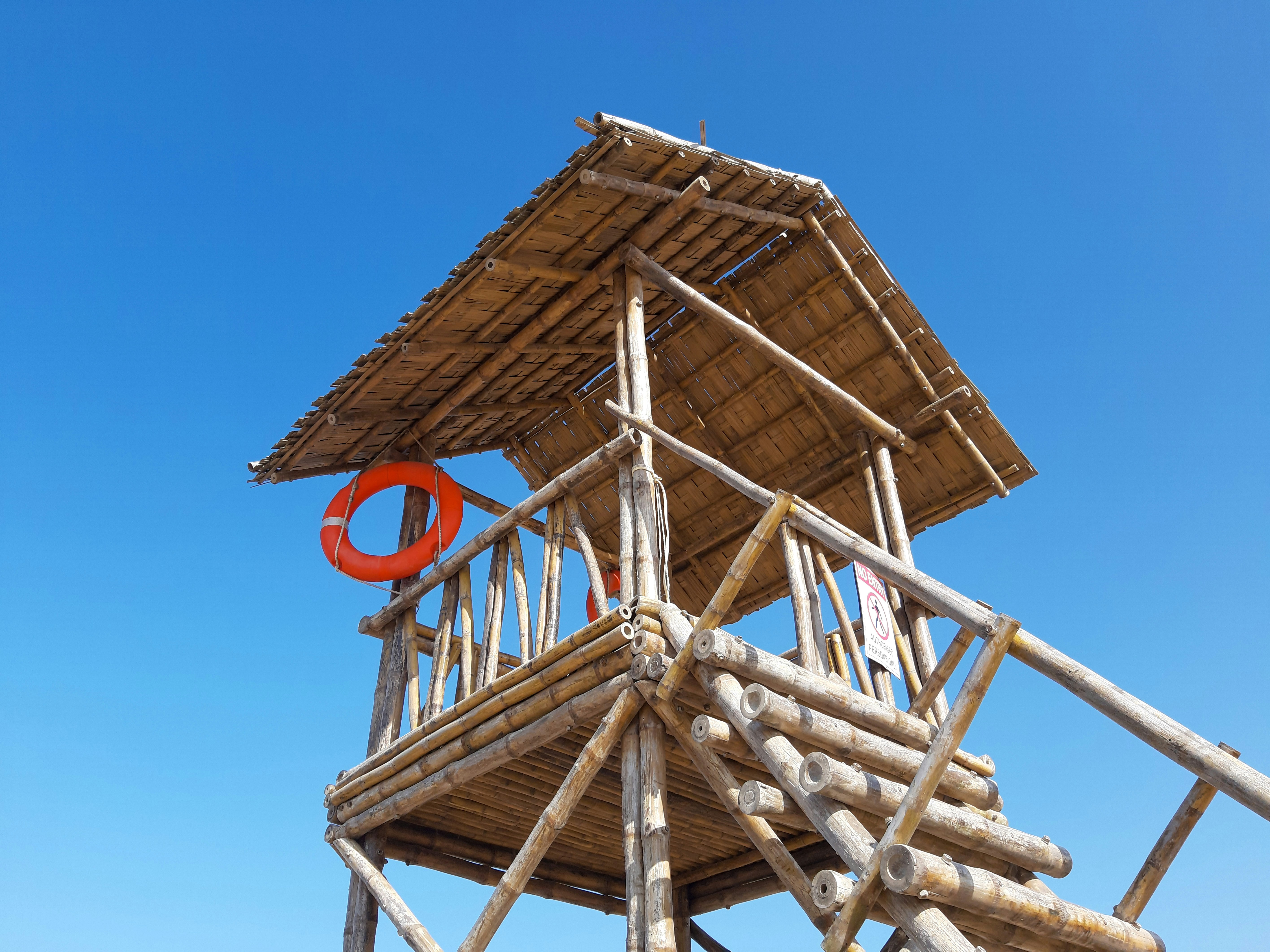 Wooden lifeguard tower overlooking a clear blue sky, adorned with a bright orange buoy. Perfectly positioned for beach safety.