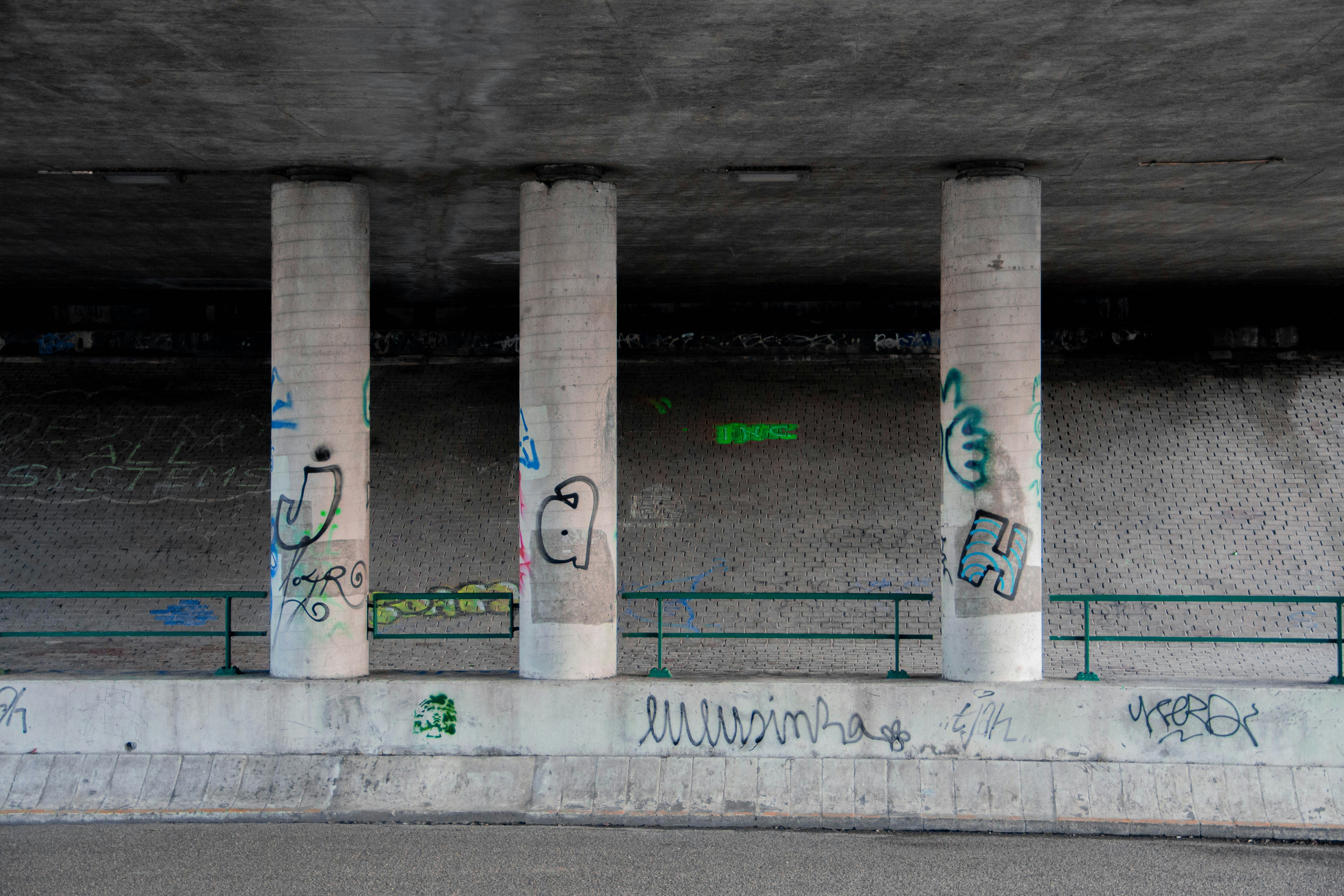 Concrete pillars adorned with vibrant graffiti under a bridge, showcasing urban art and expression.