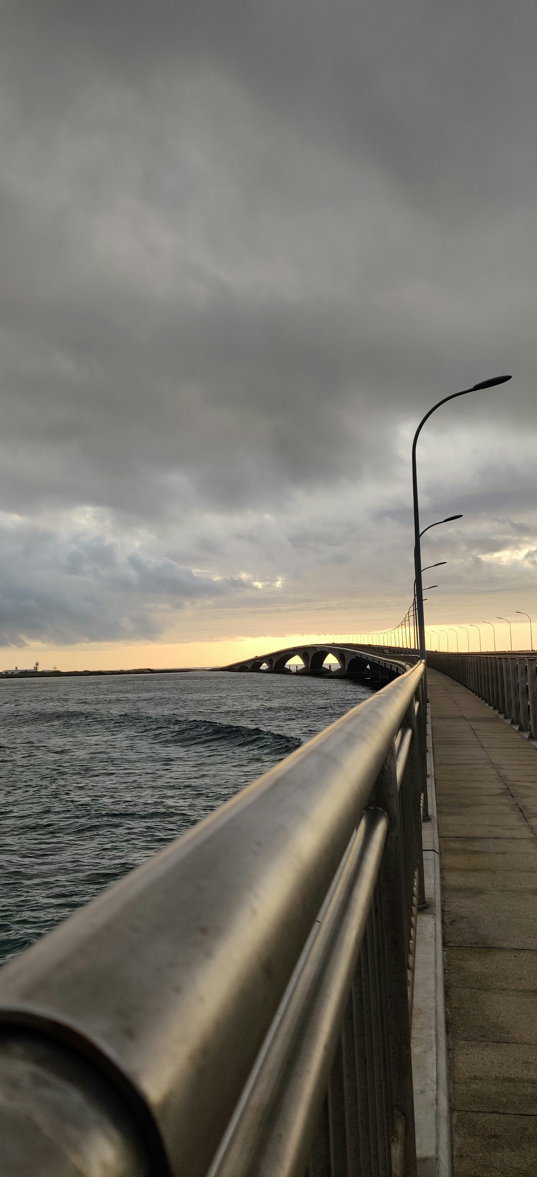 Convergence on the Pier: A Walk Toward the Distant Bridge Under Moody Skies