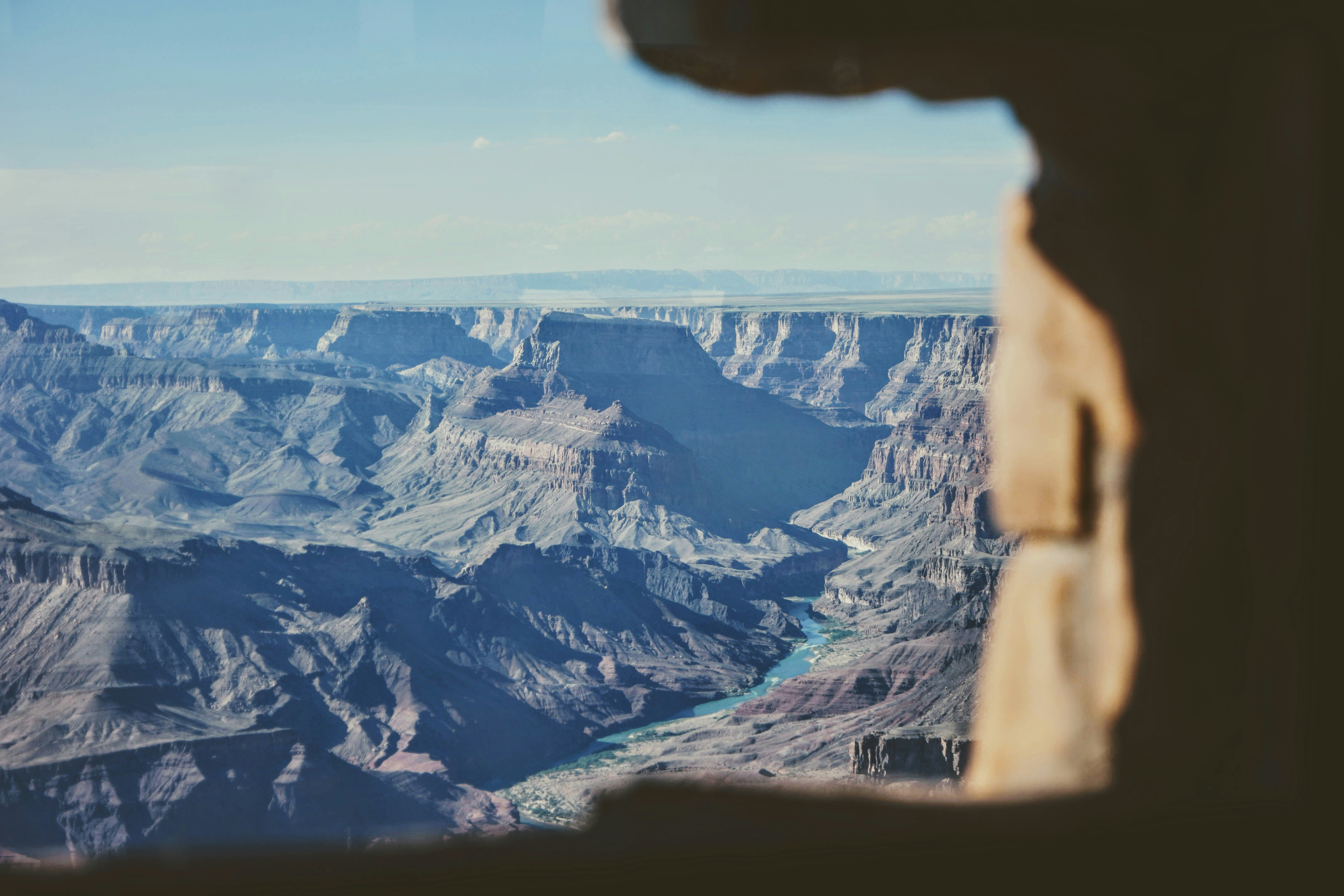 Expansive view of the Grand Canyon framed by rocky outcrop, showcasing the winding river below and layered geological formations. 
