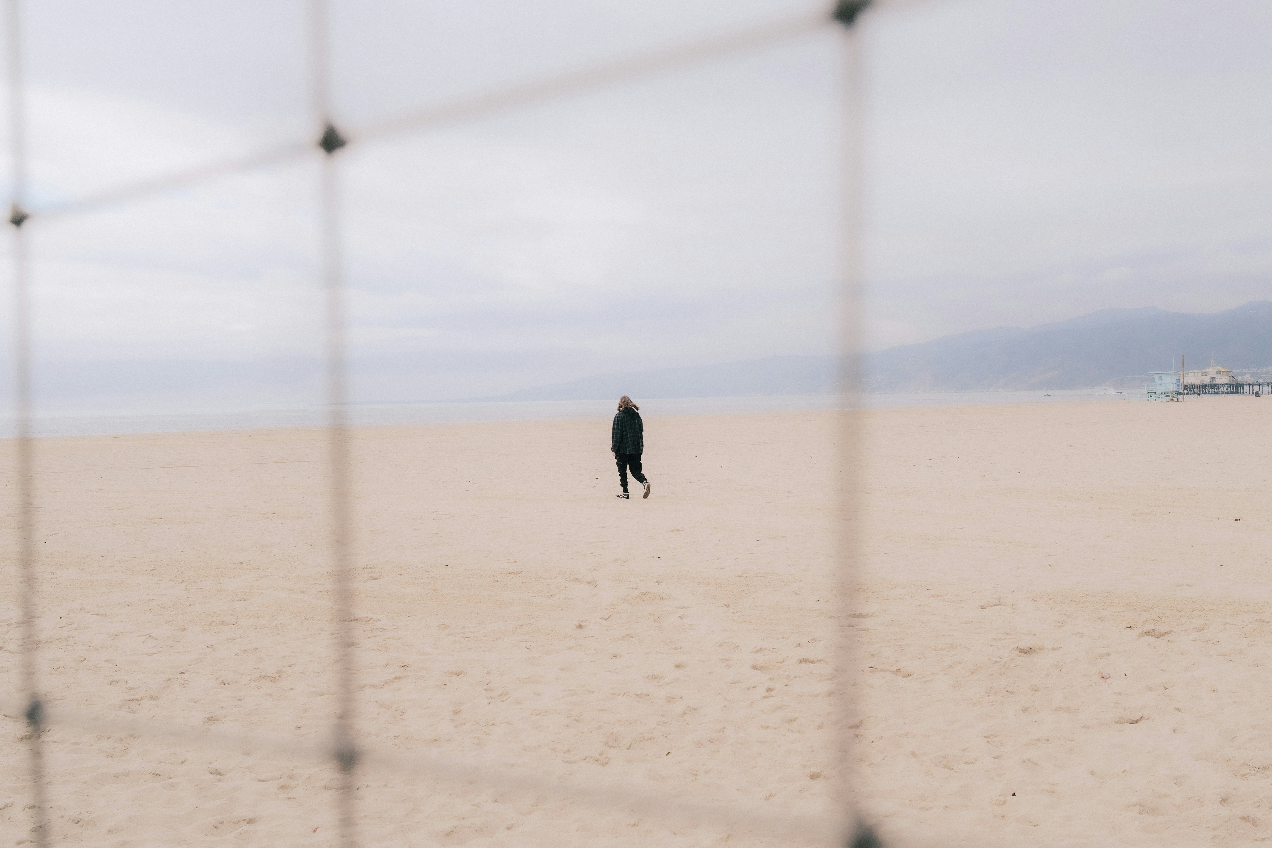 Solitary Figure on an Expansive Beach Framed by Chain Link