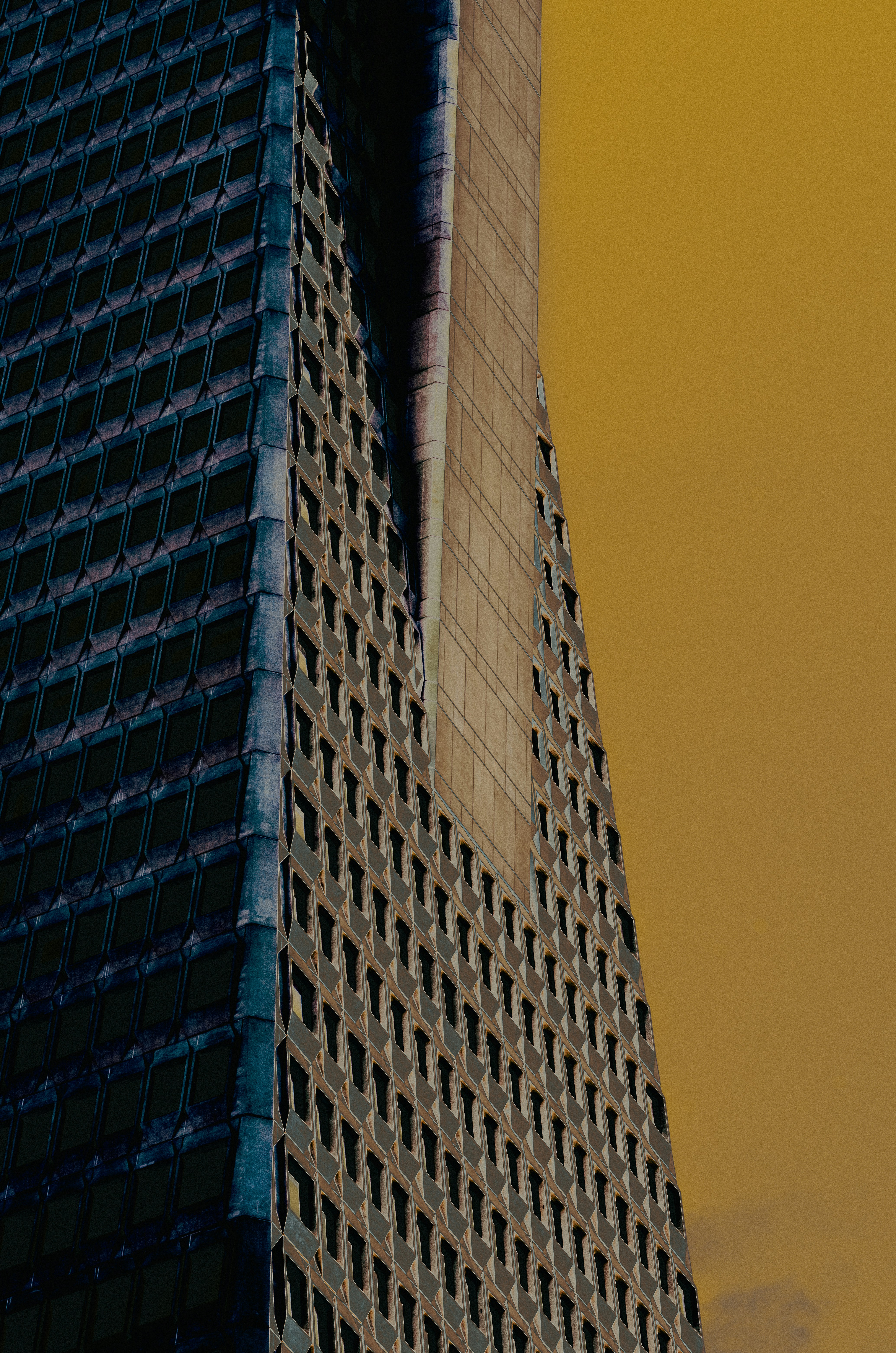 Close-up of a modern skyscraper showcasing geometric patterns and textures, contrasted by a warm golden sky.