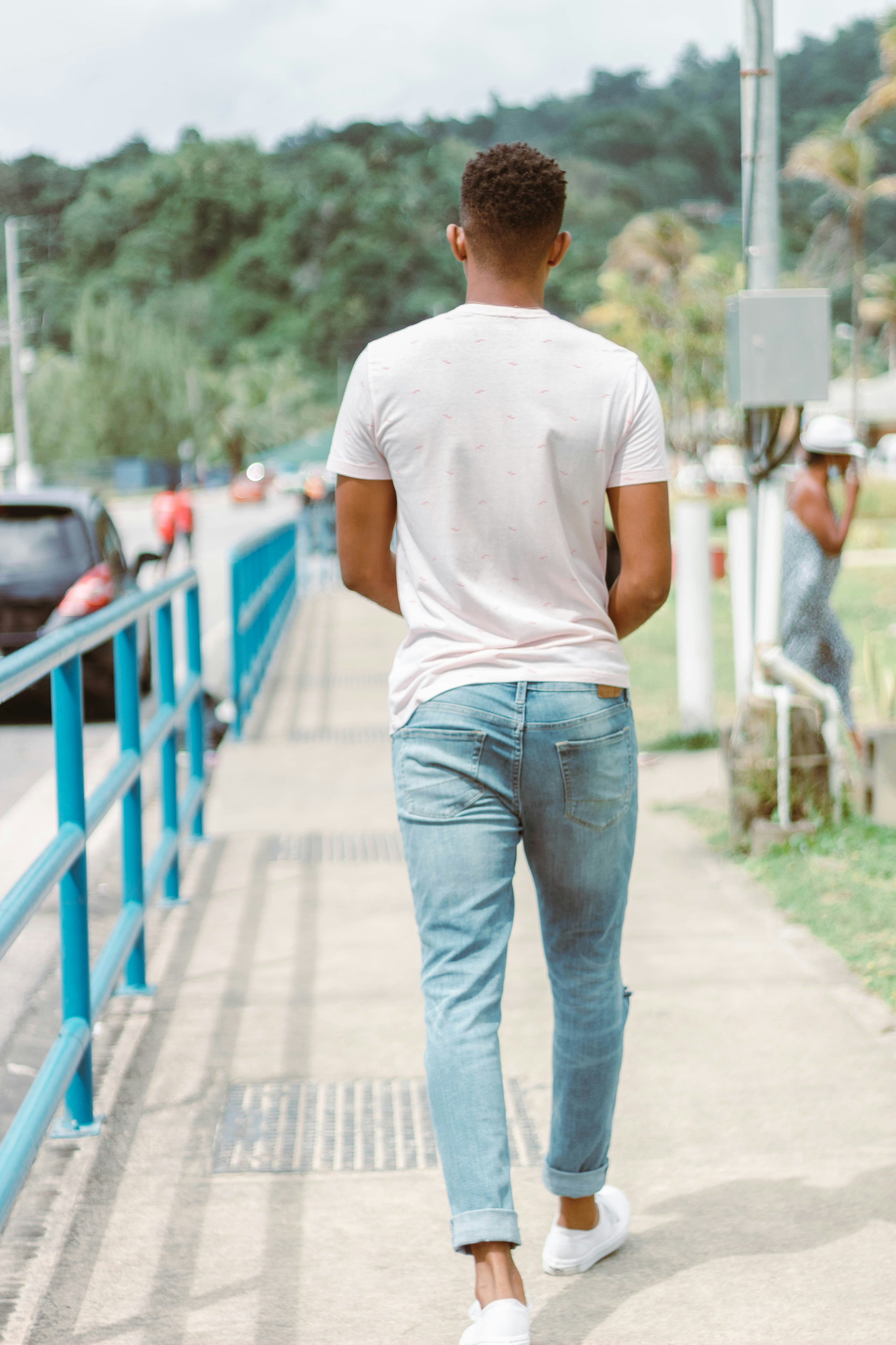 Young man walking along a bustling sidewalk, framed by colorful surroundings and a glimpse of nature in the background.