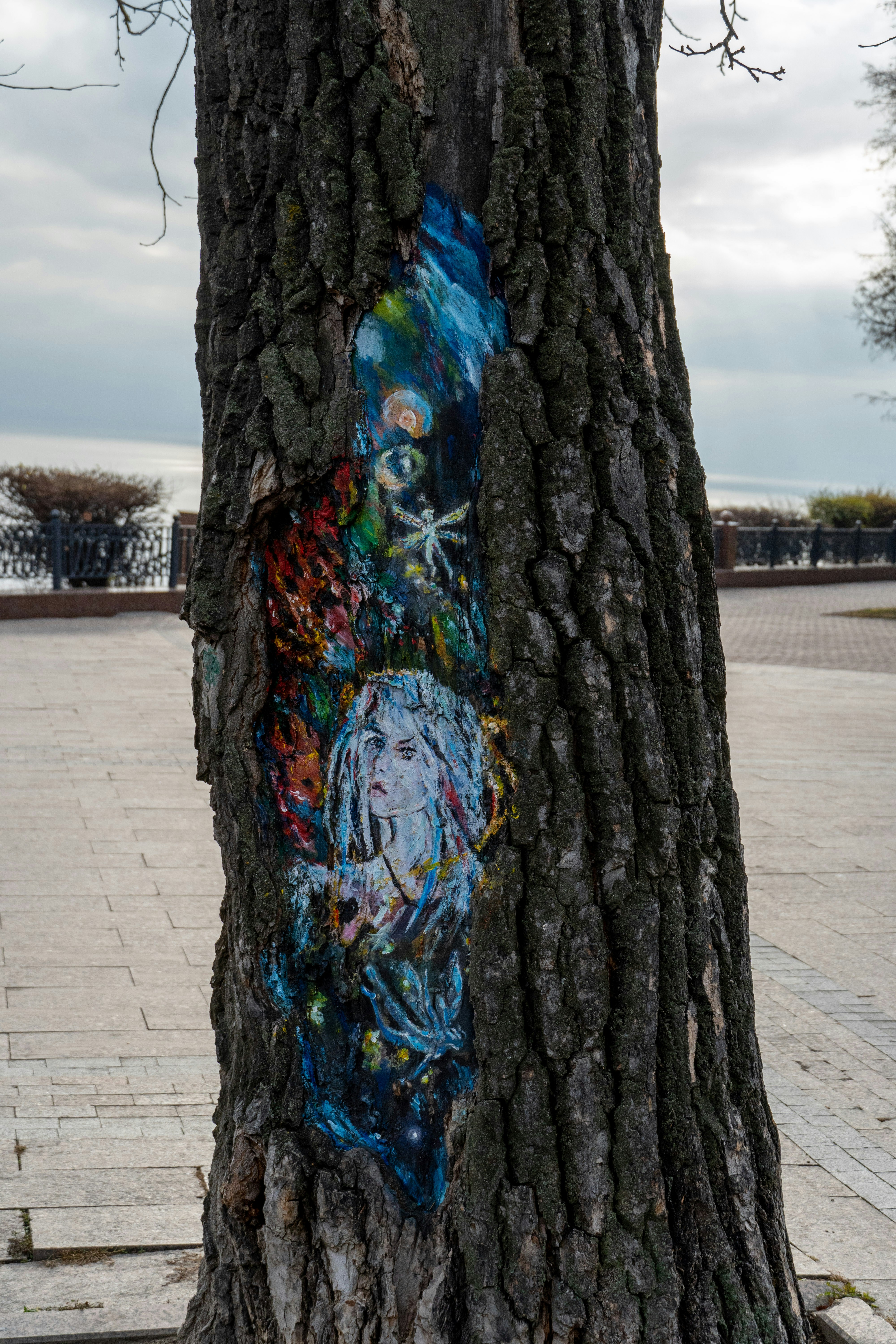Vibrant mural painted on a tree trunk, depicting a mystical figure surrounded by colorful swirls and celestial elements.