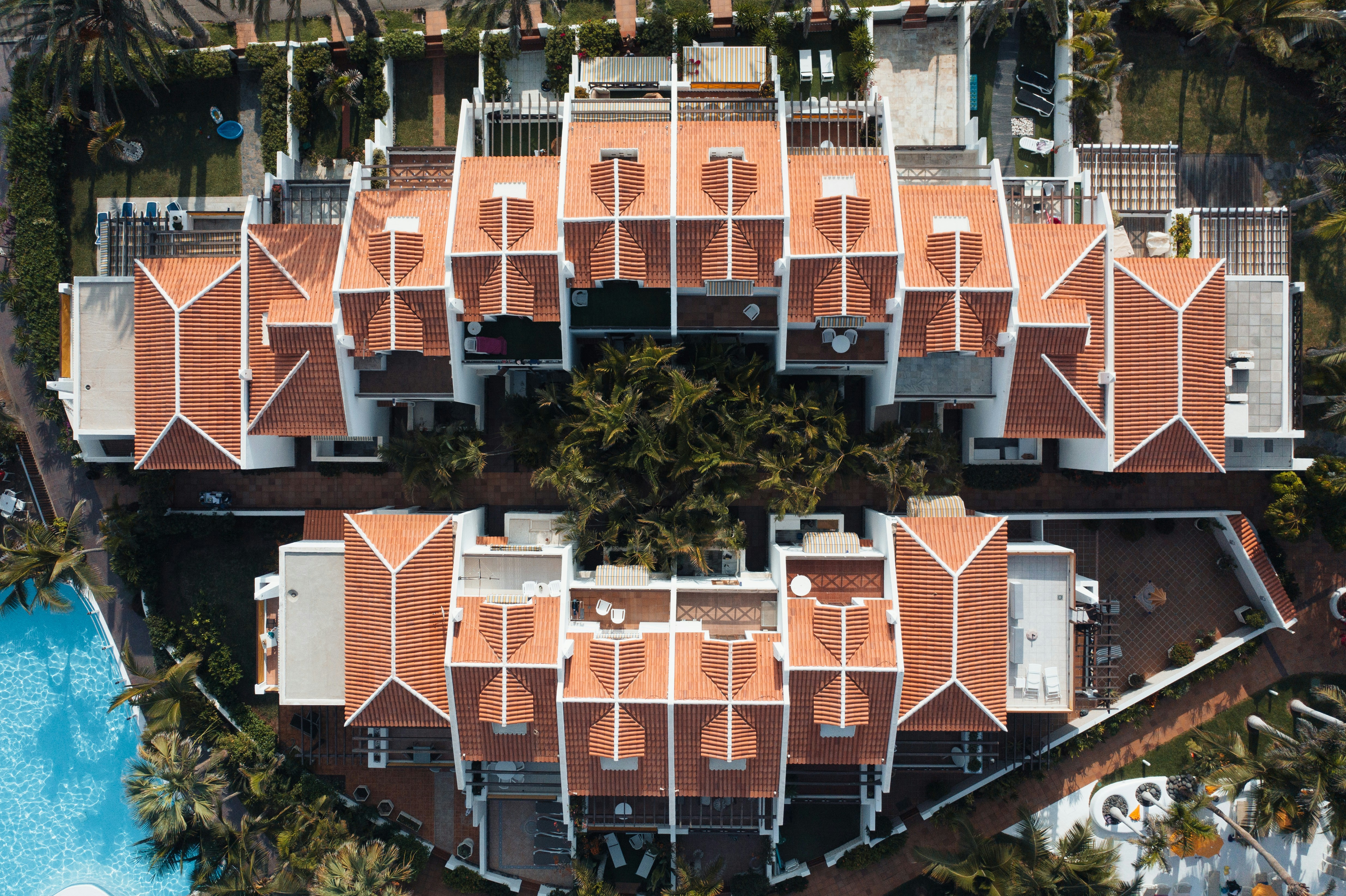 Aerial view of a resort complex showcasing terracotta-roofed villas surrounded by lush greenery and a sparkling pool.