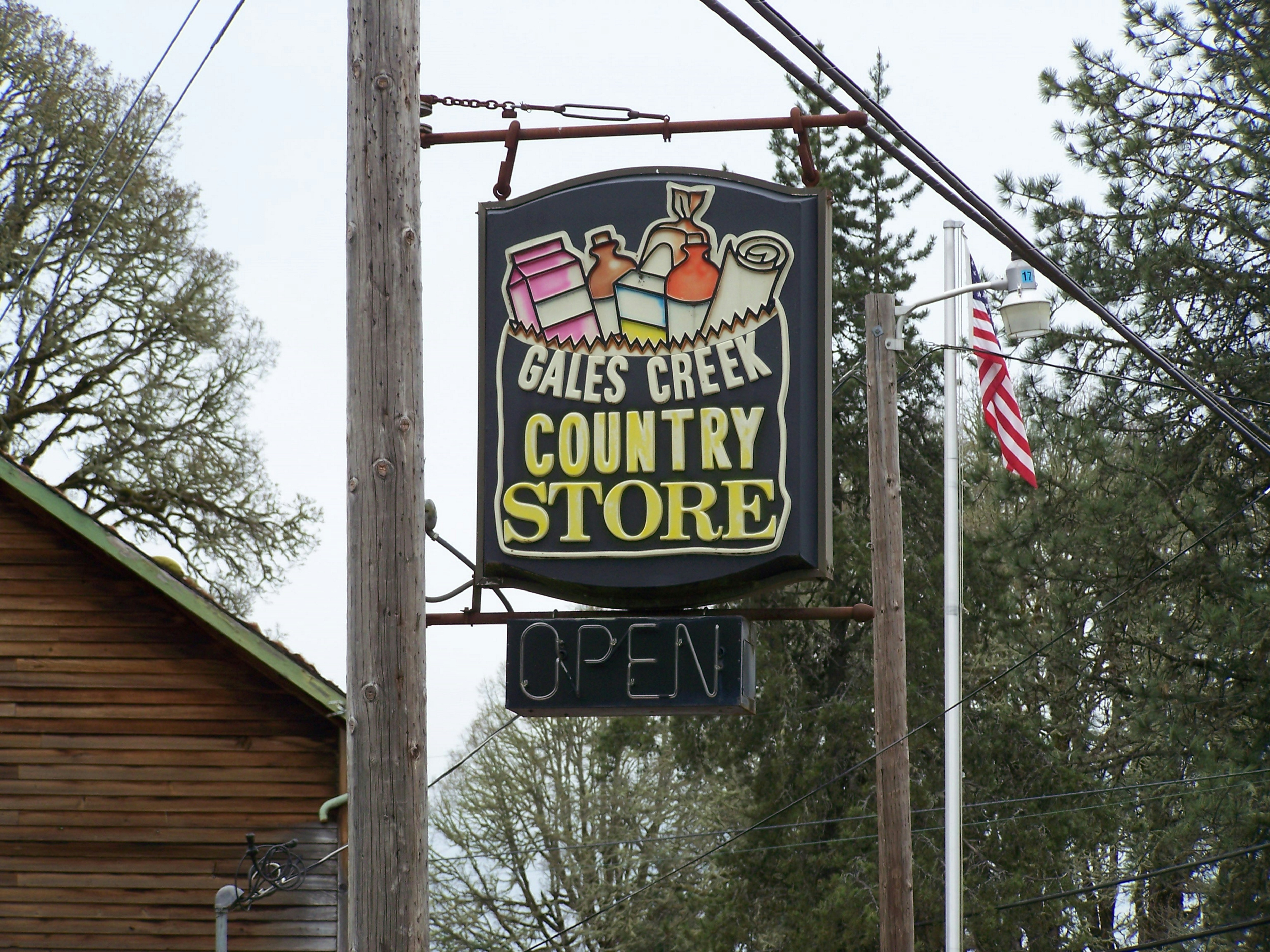 Gales Creek Country Store sign with colorful imagery against a backdrop of trees and an American flag.