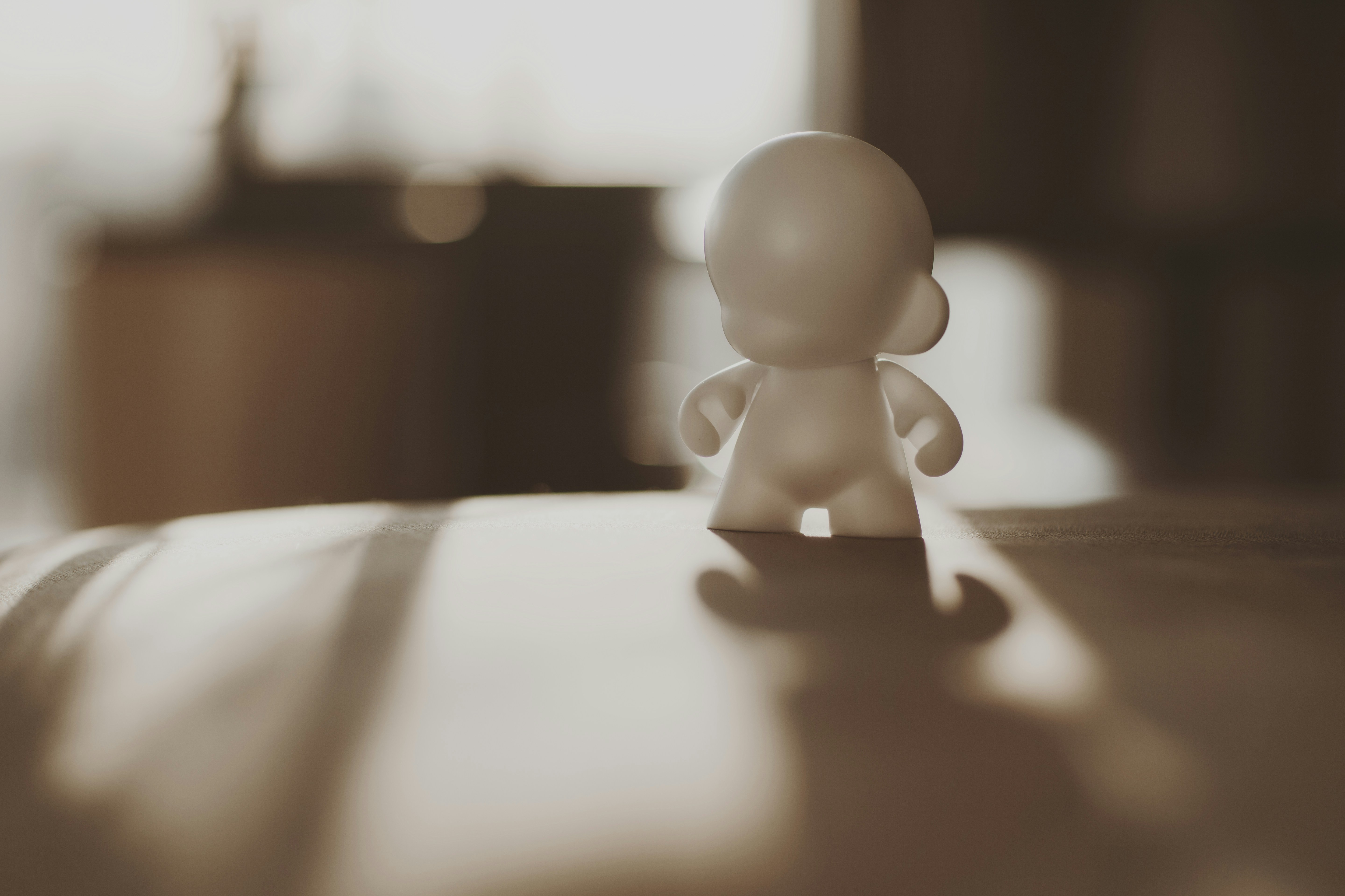 Minimalist figurine standing on a soft surface, casting a long shadow in warm, diffused light.