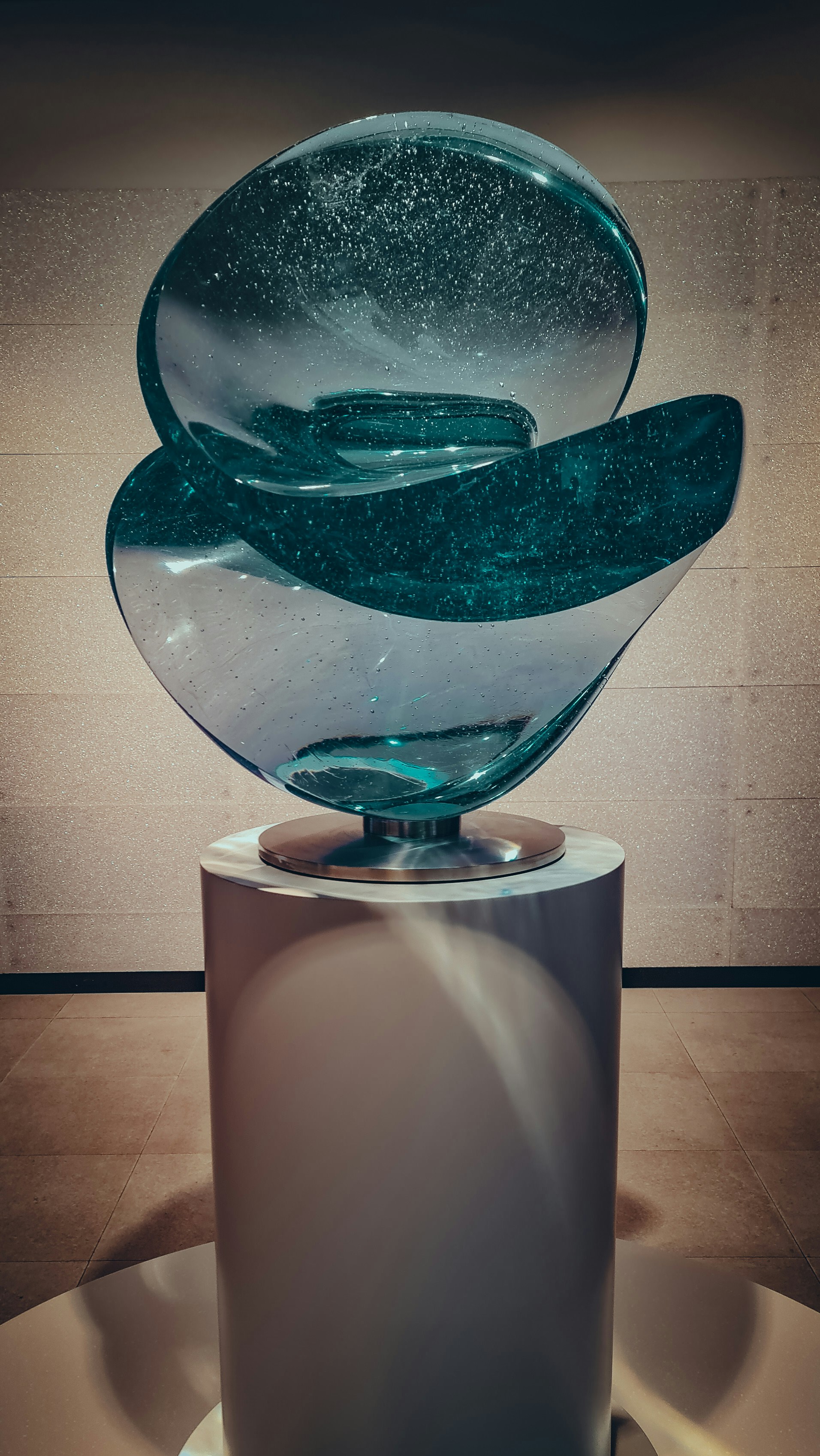 Glass Sculpture in Soft Spotlight: A Teal Spiral on a Concrete Pedestal