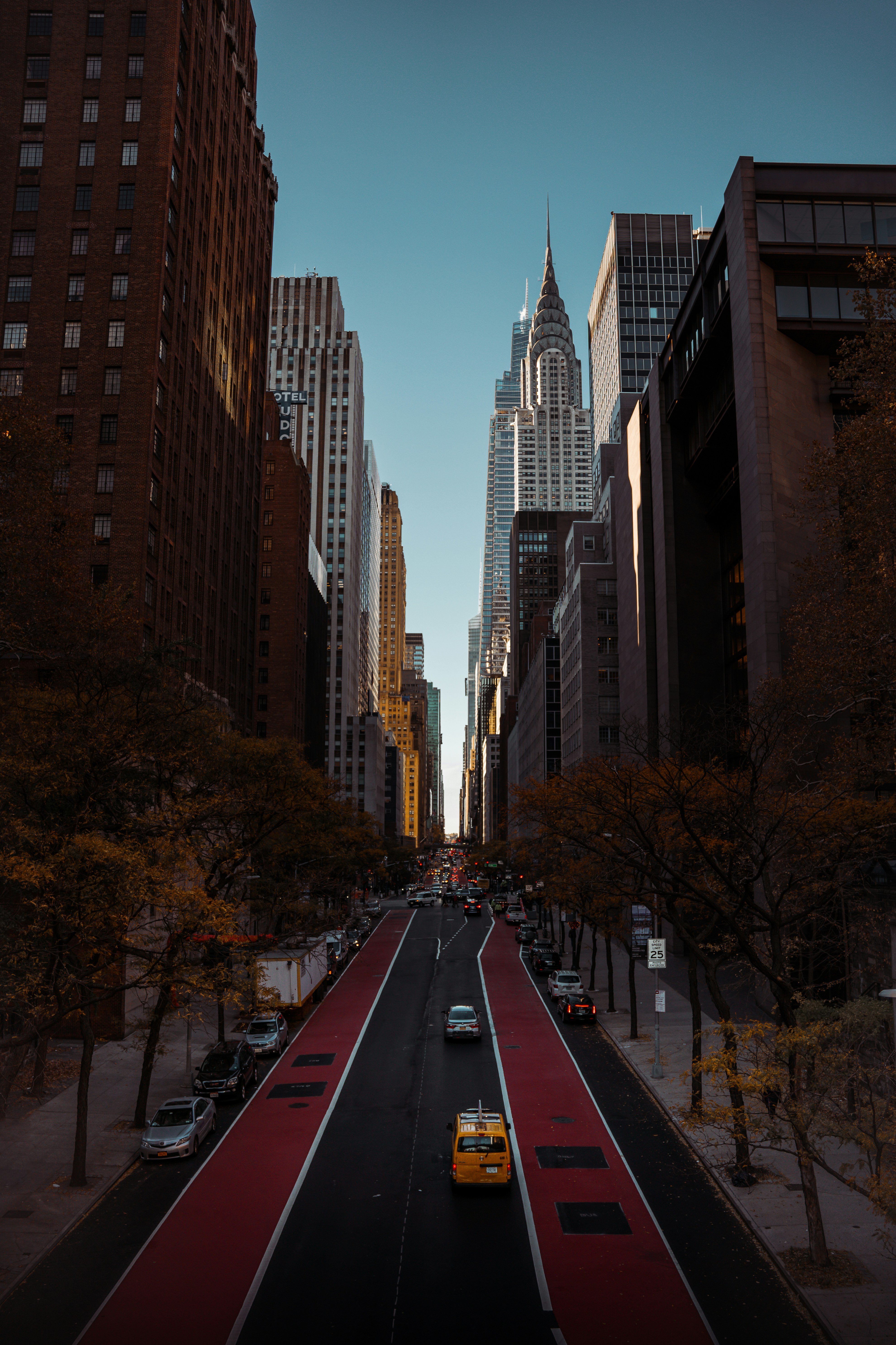 Manhattan street with red bus lanes and a yellow taxi in the foreground. Tall skyscrapers frame the avenue as the eye follows toward the central spire.