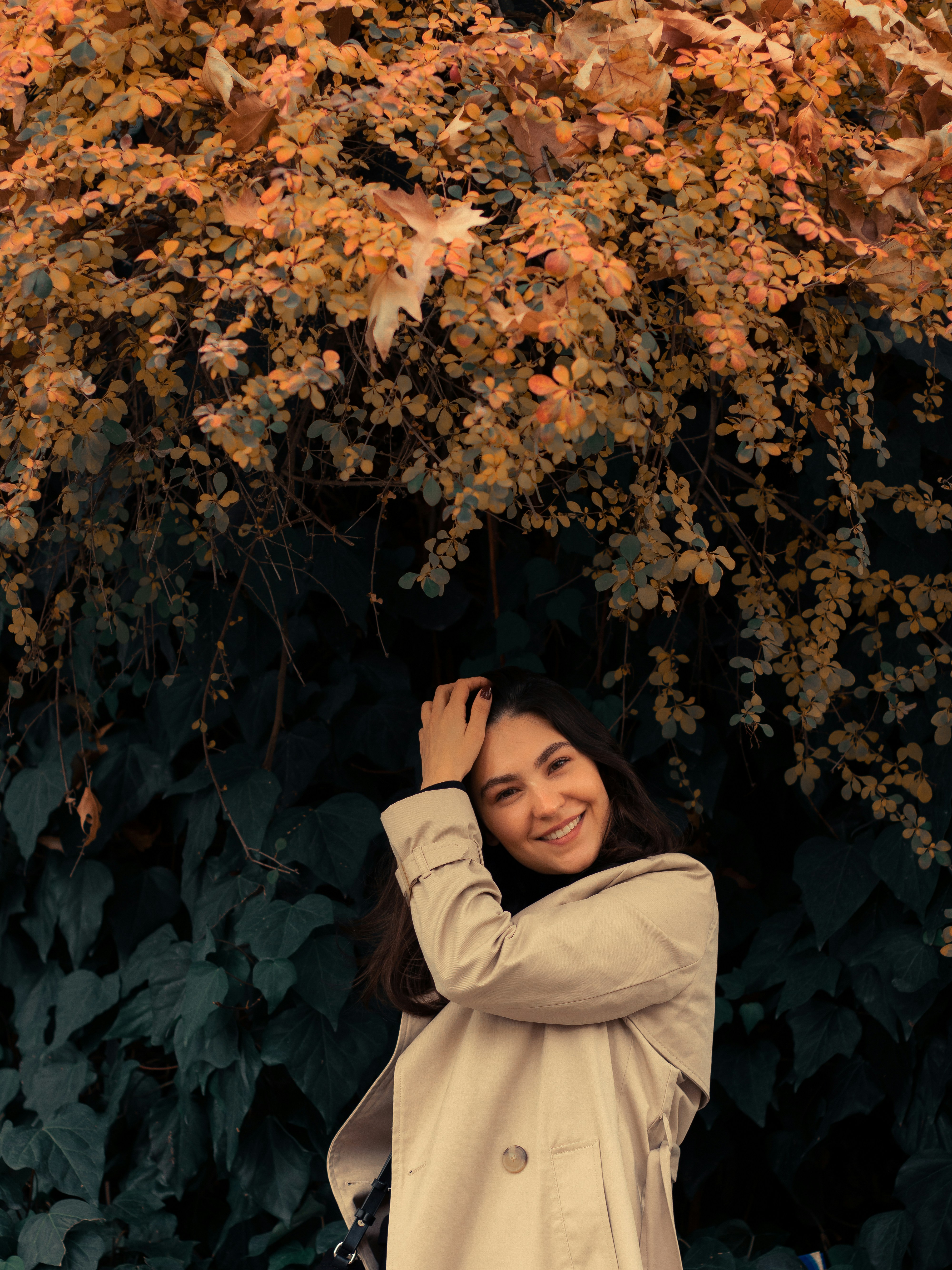 Young woman smiling beneath a cascade of autumn leaves, surrounded by lush greenery.