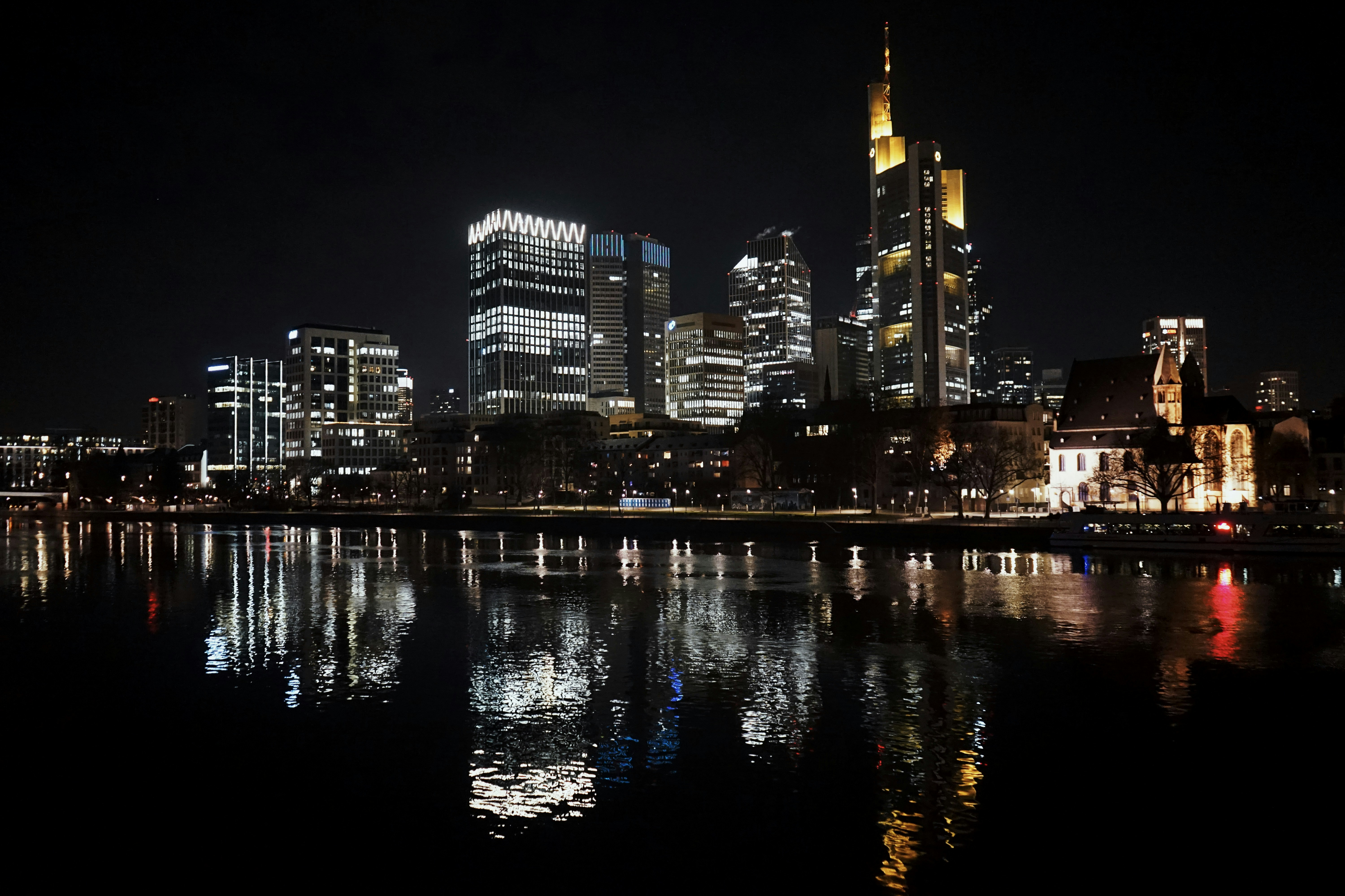 Illuminated skyline of Frankfurt at night, showcasing modern architecture and reflections on the water's surface.