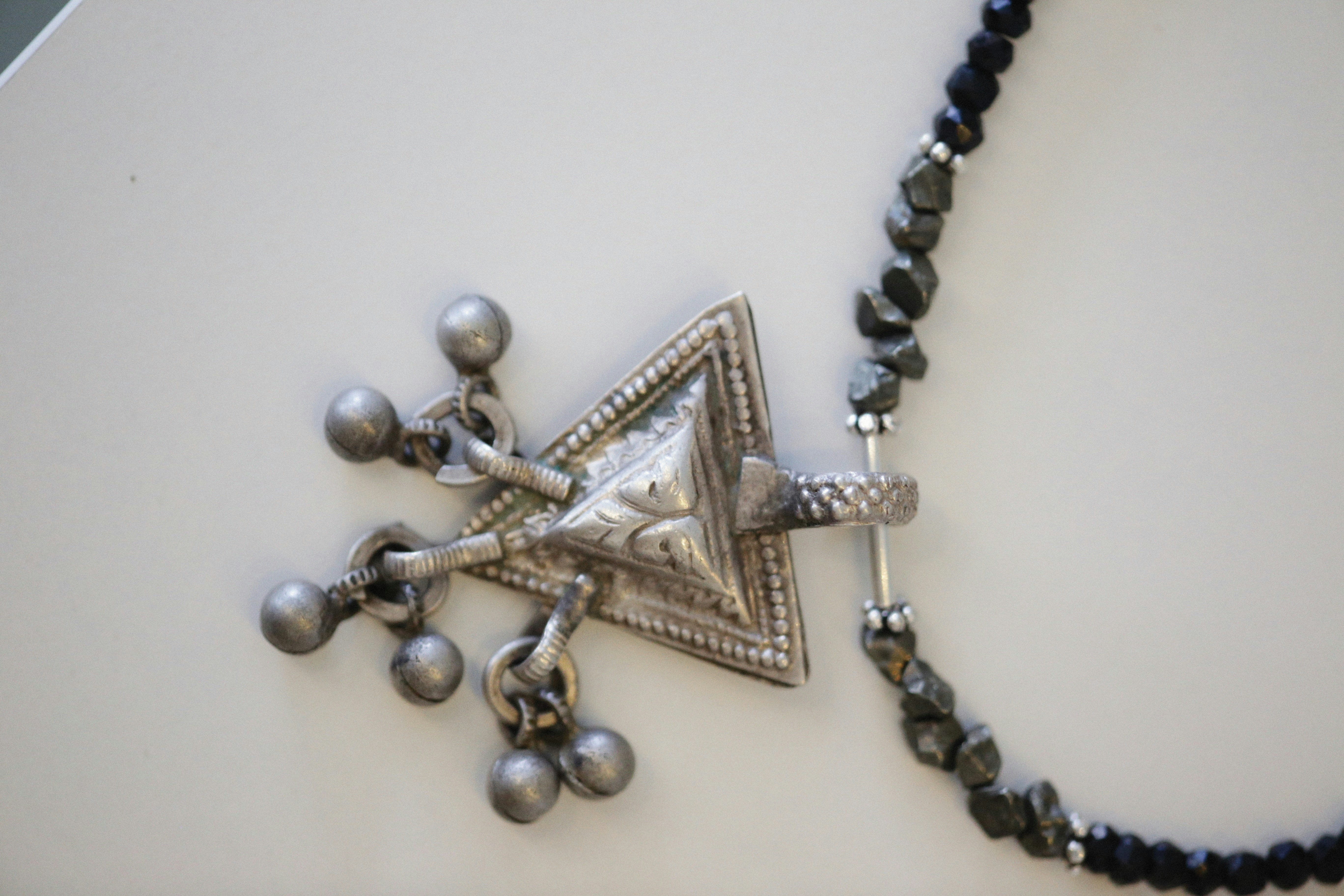 Ornate triangular pendant resting beside a beaded chain