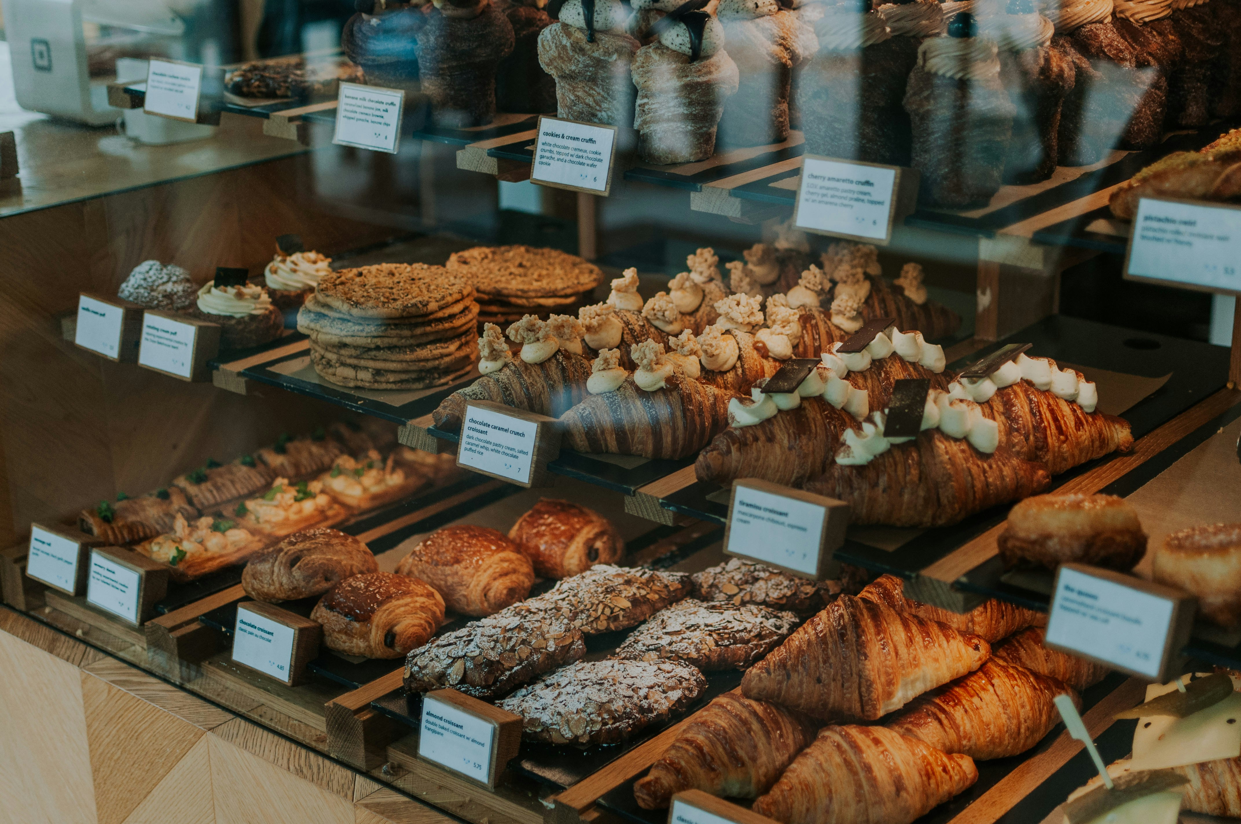 An array of beautifully crafted pastries, including croissants, cookies, and cream-topped treats, arranged enticingly in a bakery display case.