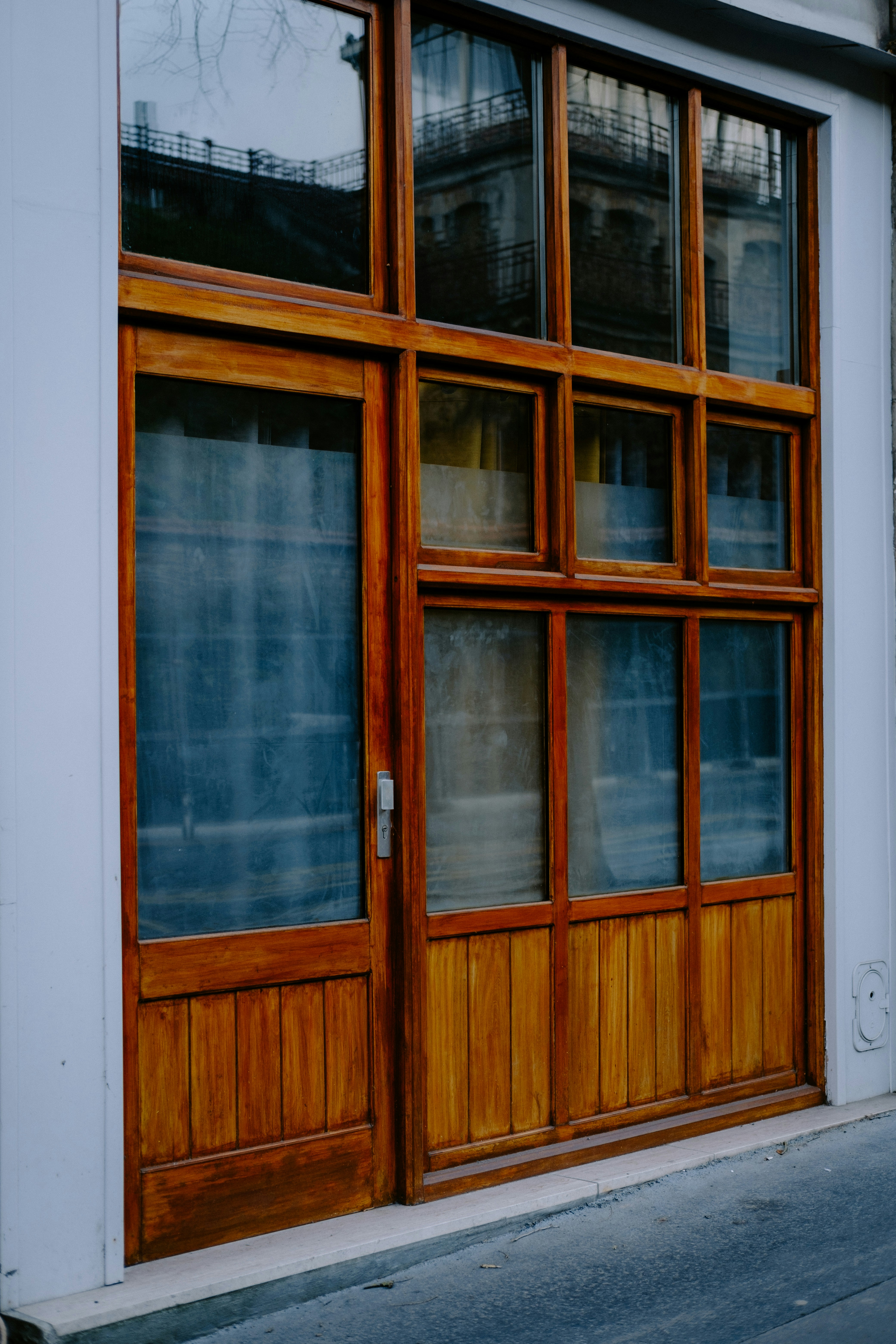 Elegant wooden door with large glass panels, framed by a minimalist wall, showcasing urban architectural design.