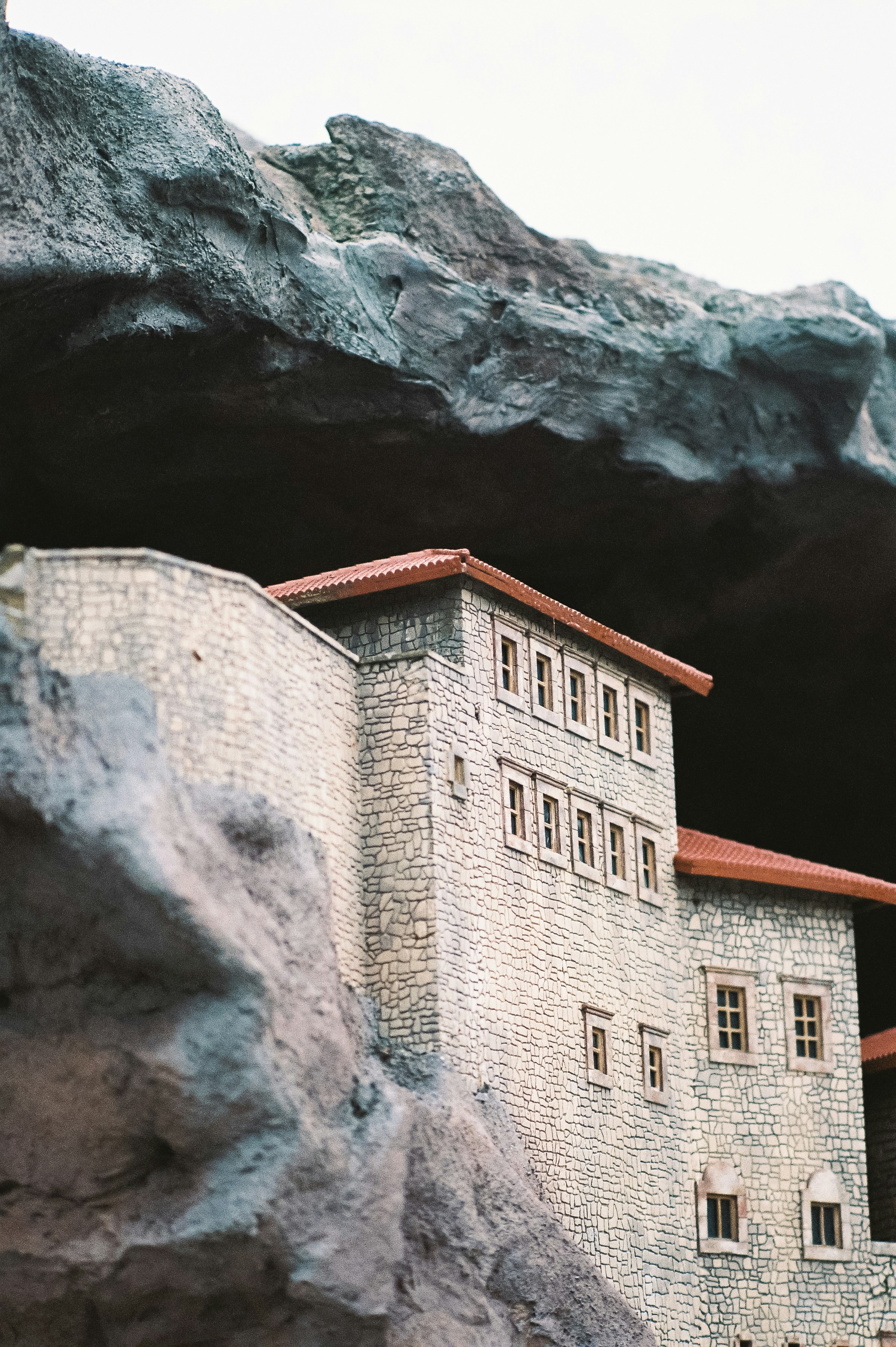 Stone-built structure tucked into a rocky cliff with a red-tiled roof under an overhanging formation.