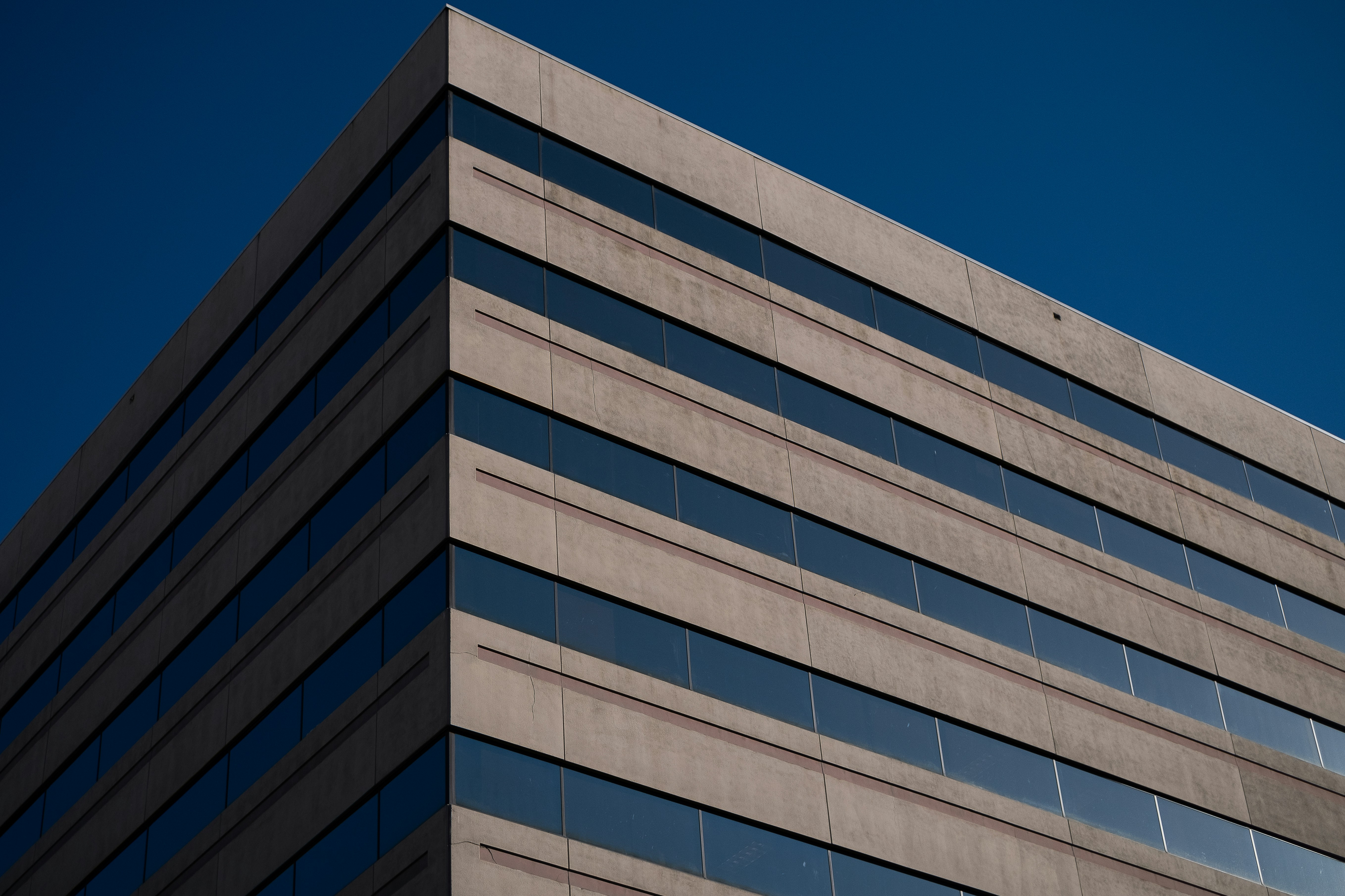 Angular view of a contemporary office building showcasing horizontal lines and reflective glass panels against a clear blue sky.