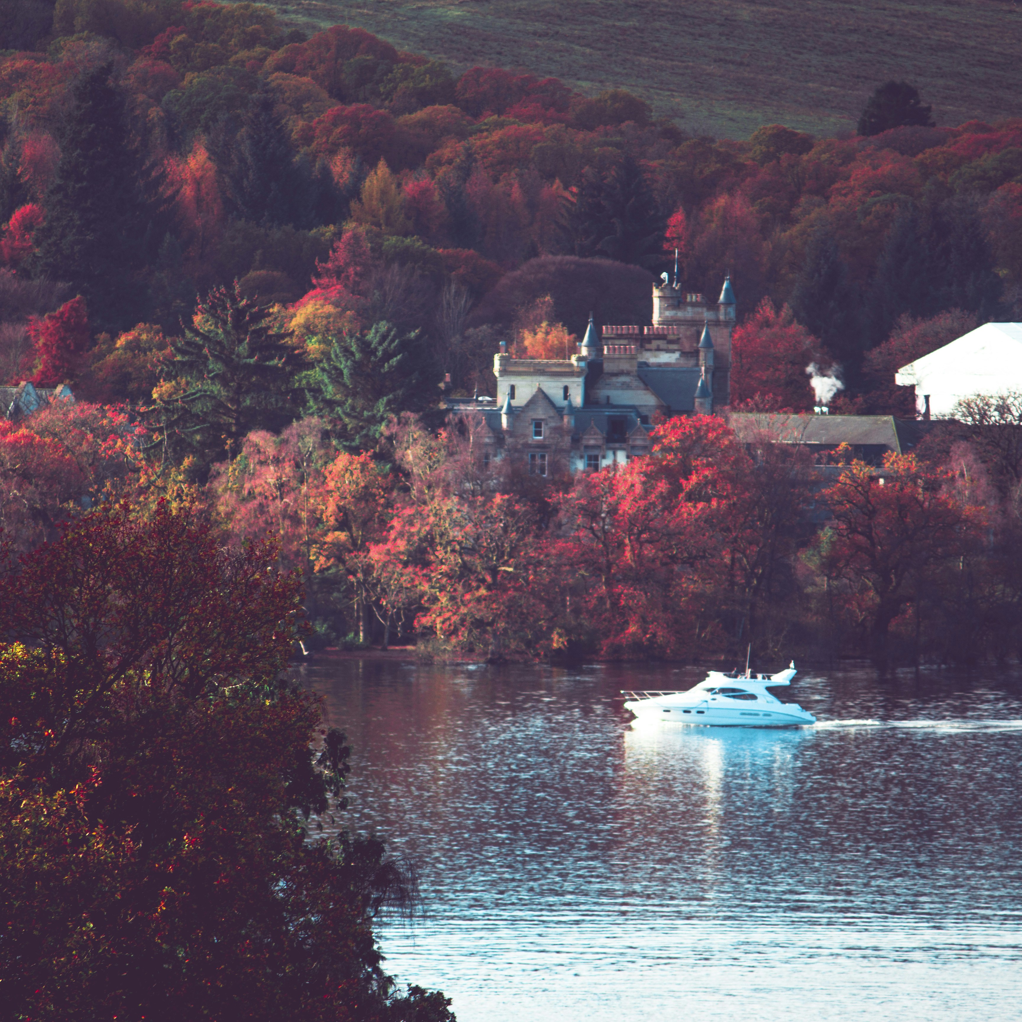 White Yacht on Autumn Lake, Framed by Ember-Tinted Forest and a Lakeside Castle