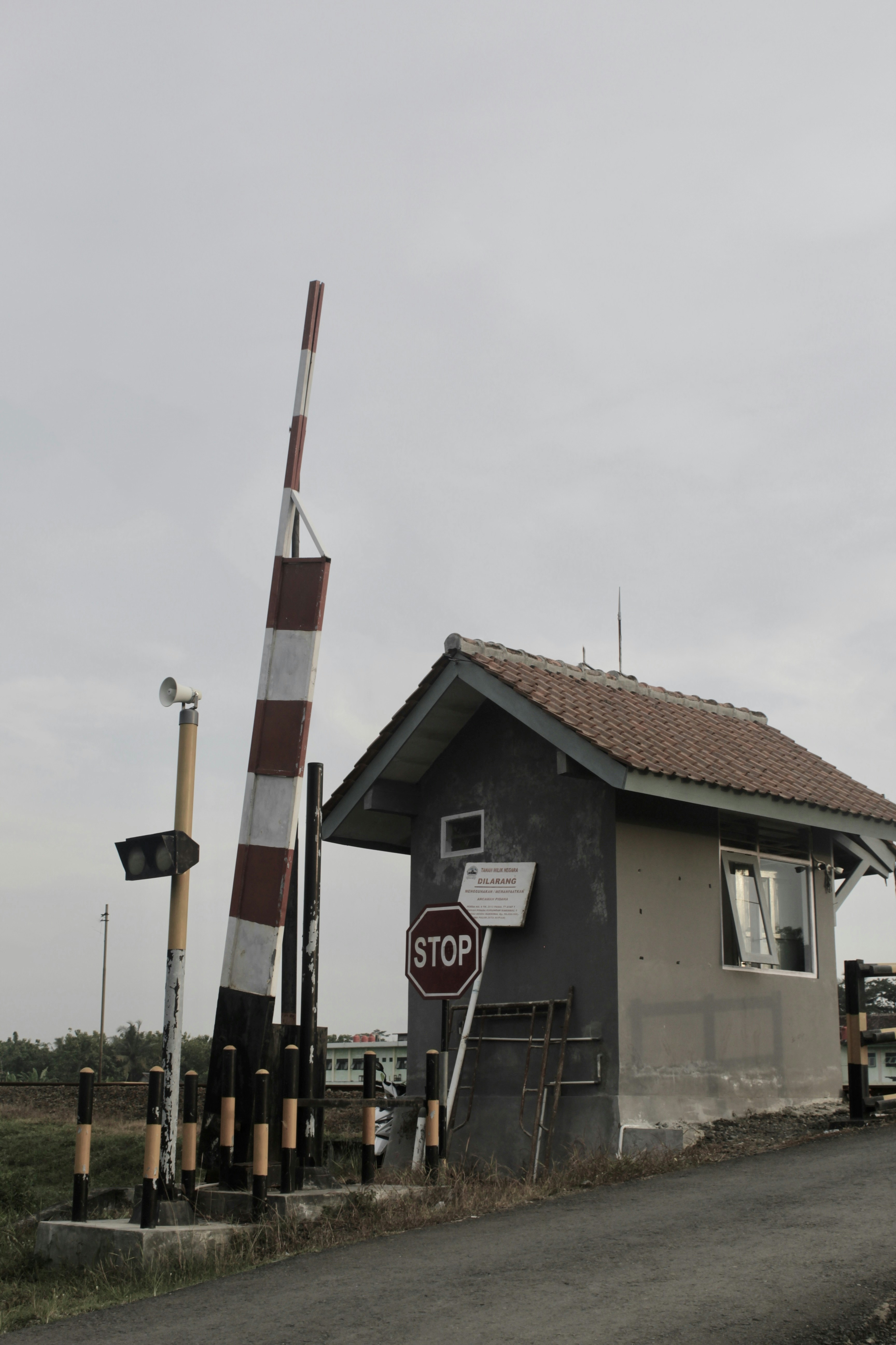 A stop gate structure with a striped barrier and a stop sign, set against a cloudy sky, indicating a controlled entry point. The scene captures an intersection of transportation and security.