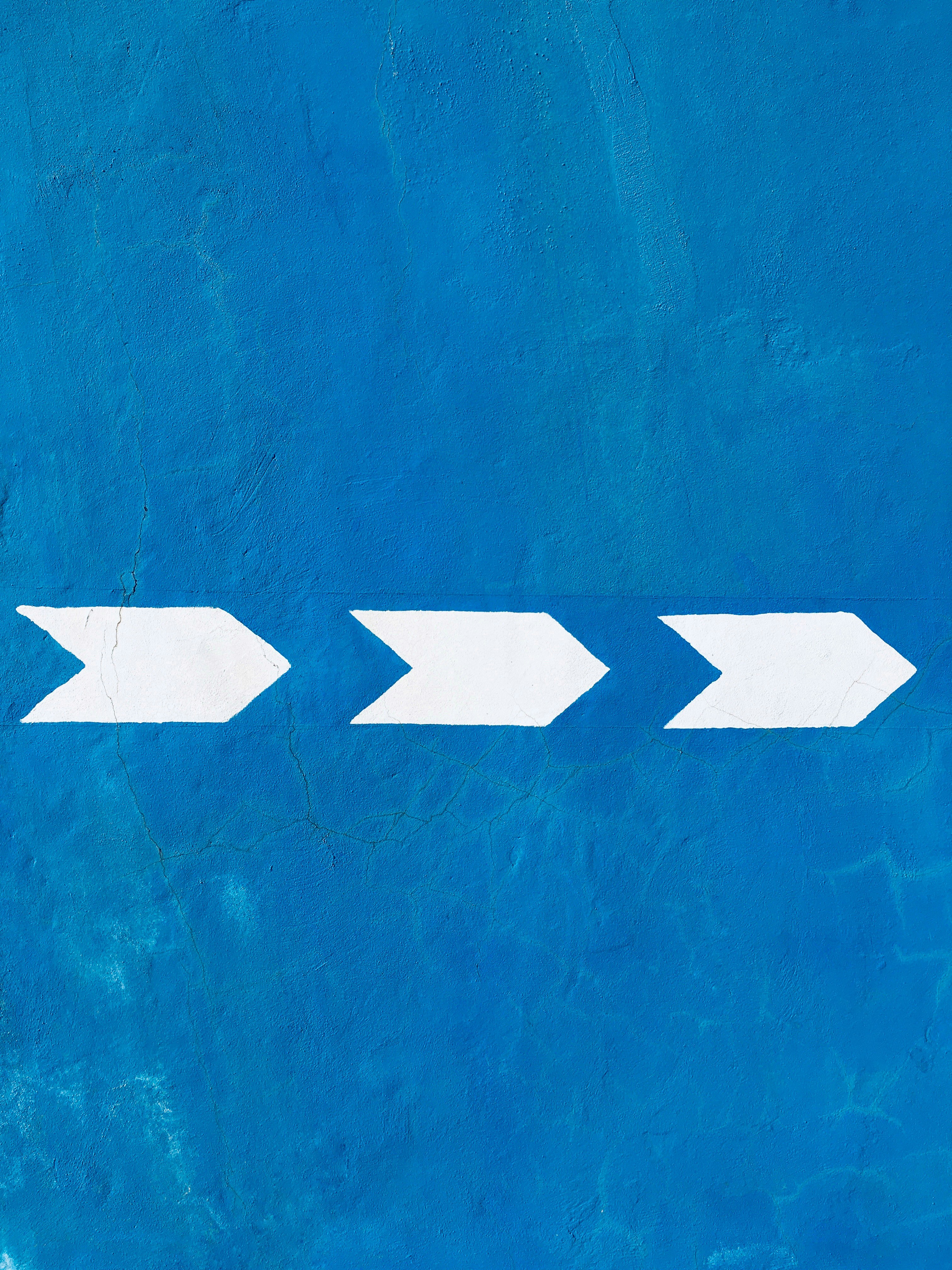 White arrows painted on a vibrant blue wall, suggesting movement and direction. The contrast highlights the simplicity and clarity of the design.