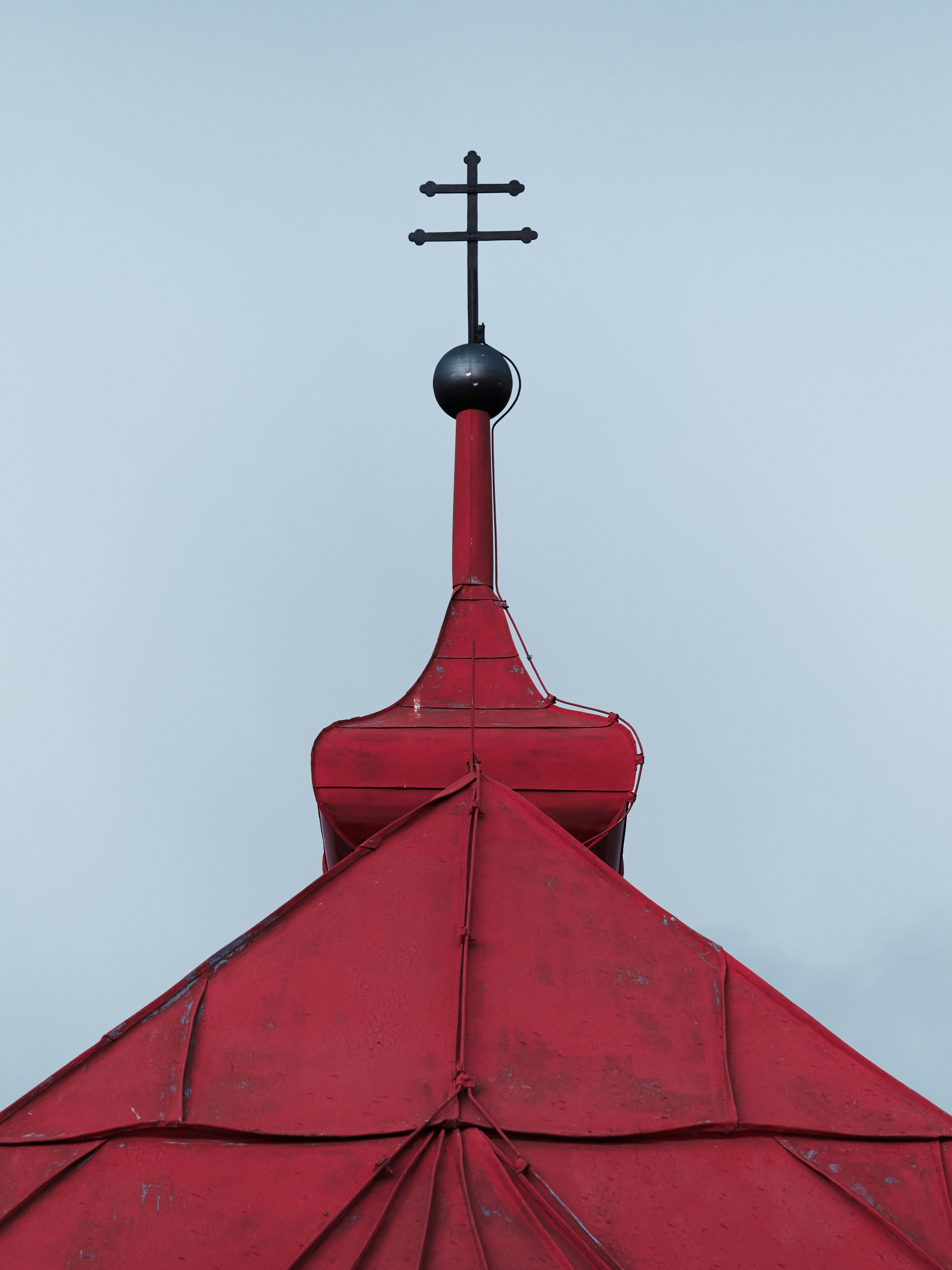 Red rooftop of a church with a distinctive cross atop, set against a pale sky.