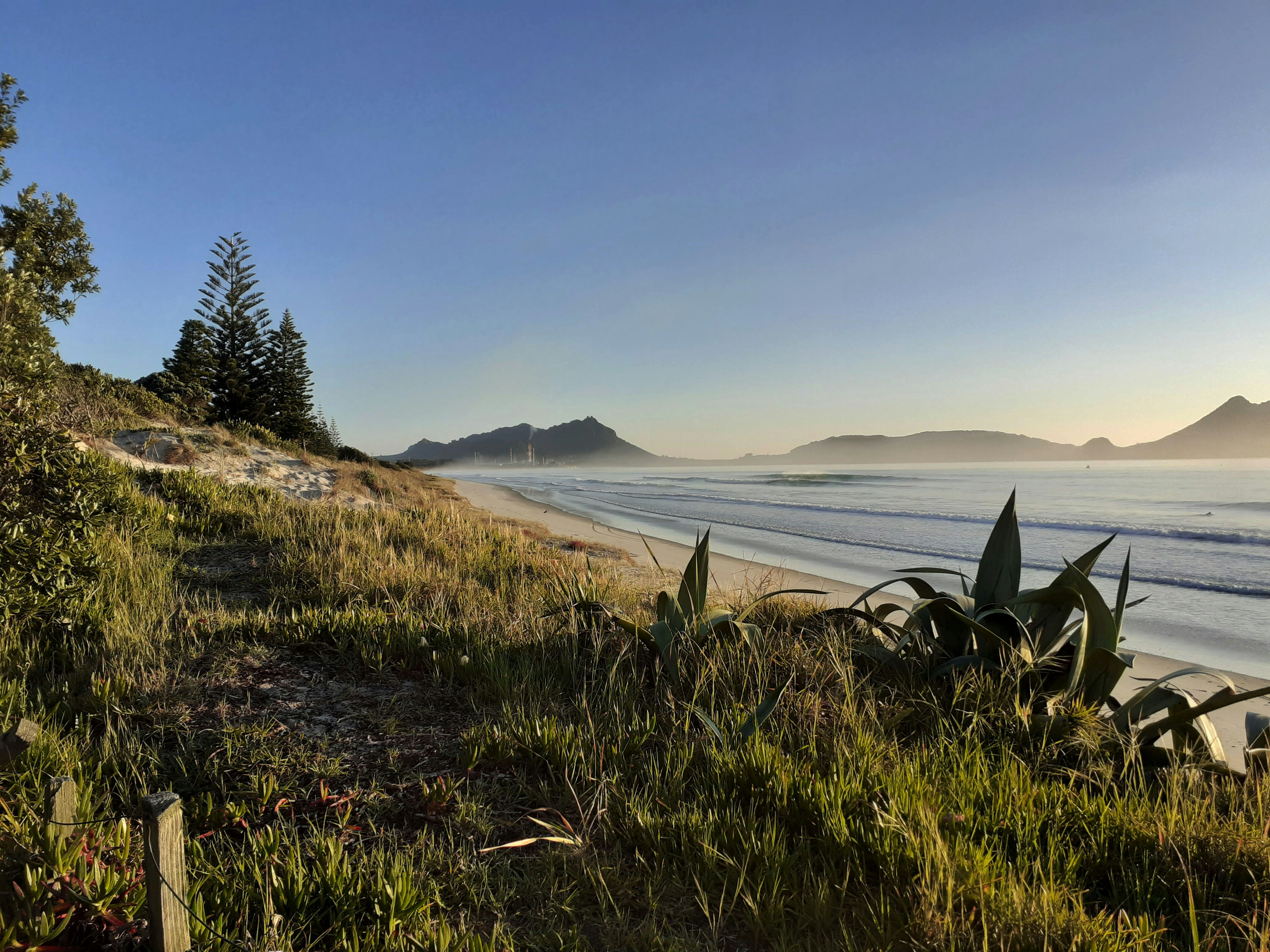 Tranquil beach scene with gentle waves lapping at the shore, framed by lush vegetation and distant mountains. 