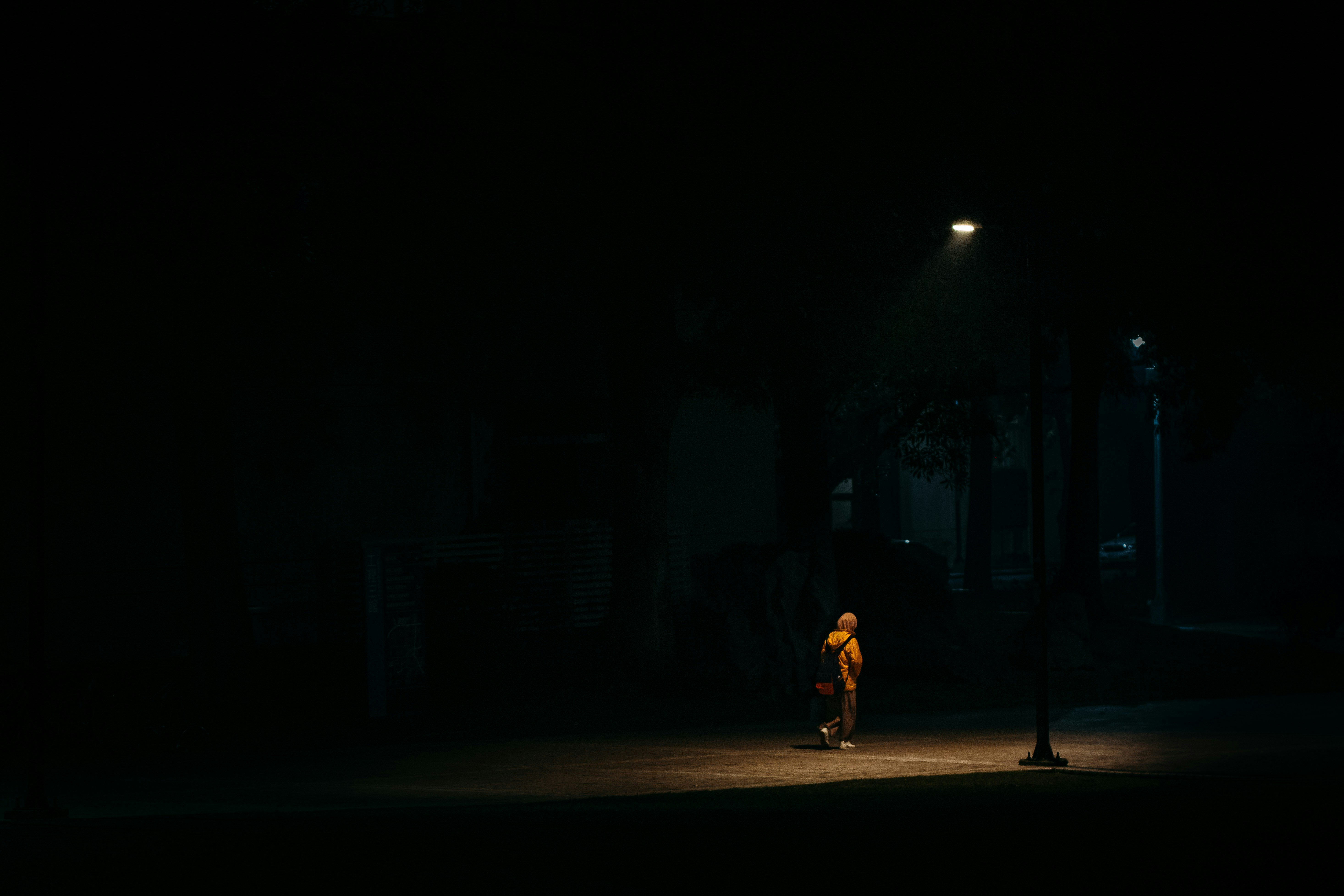 A child in a yellow jacket walks alone beneath a streetlamp in a dark urban setting, creating a poignant contrast between light and shadow.