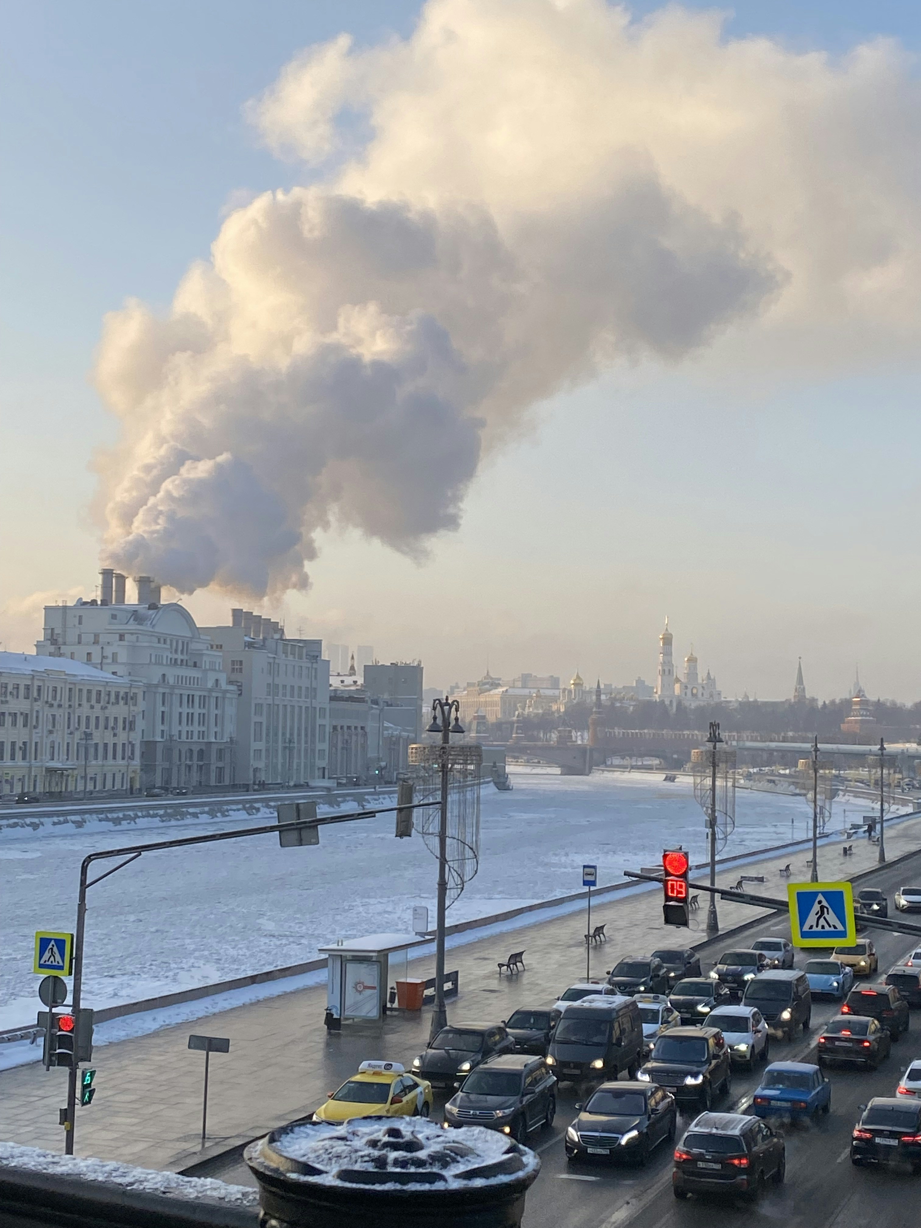 Vent of Winter: Smoke Drifts Over a Snowbound Riverfront as Traffic Flows Through a Quiet Industrial City